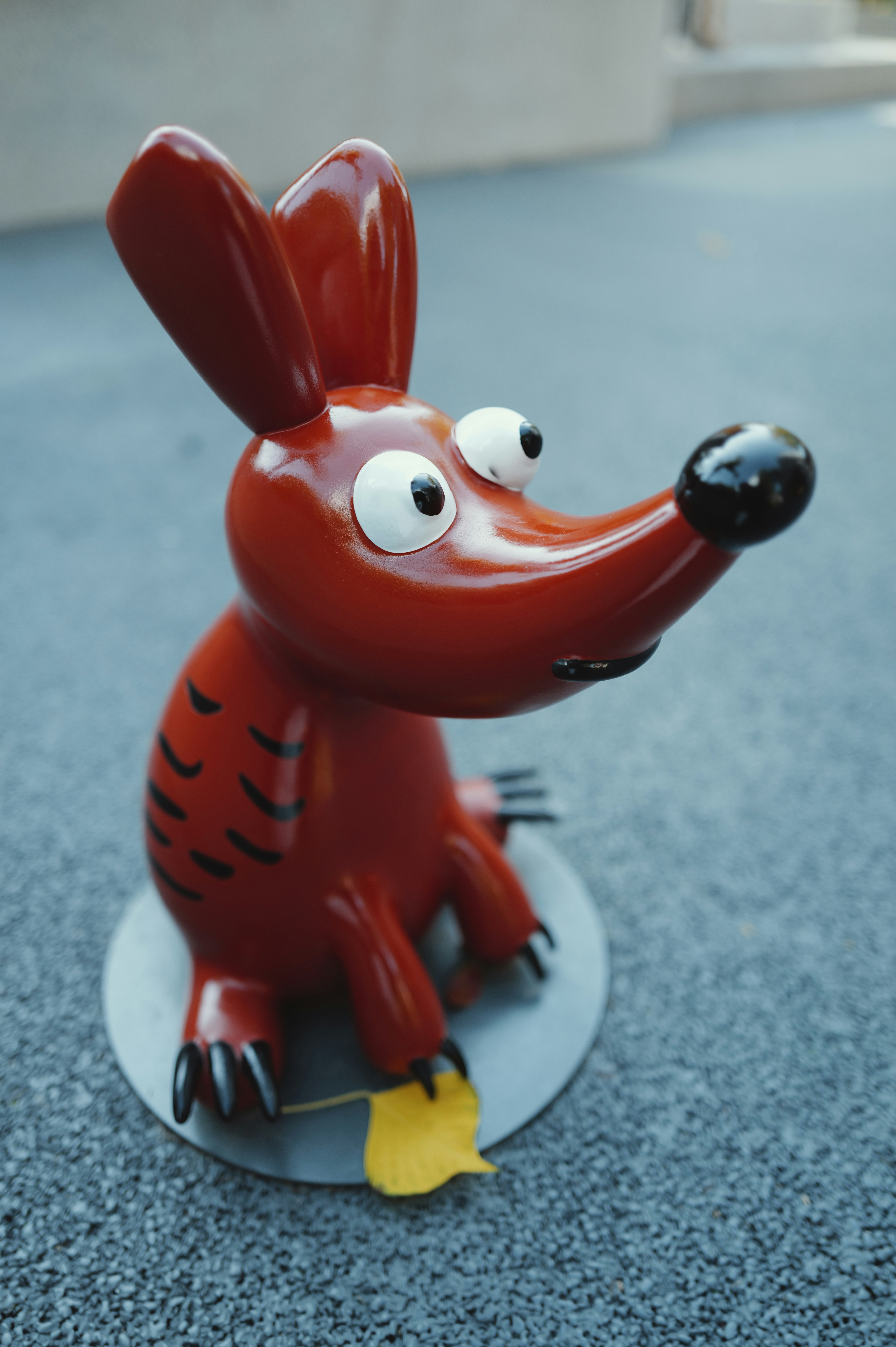 Glossy Red Cartoon Dog Statue Perched on a Gray Playground Surface