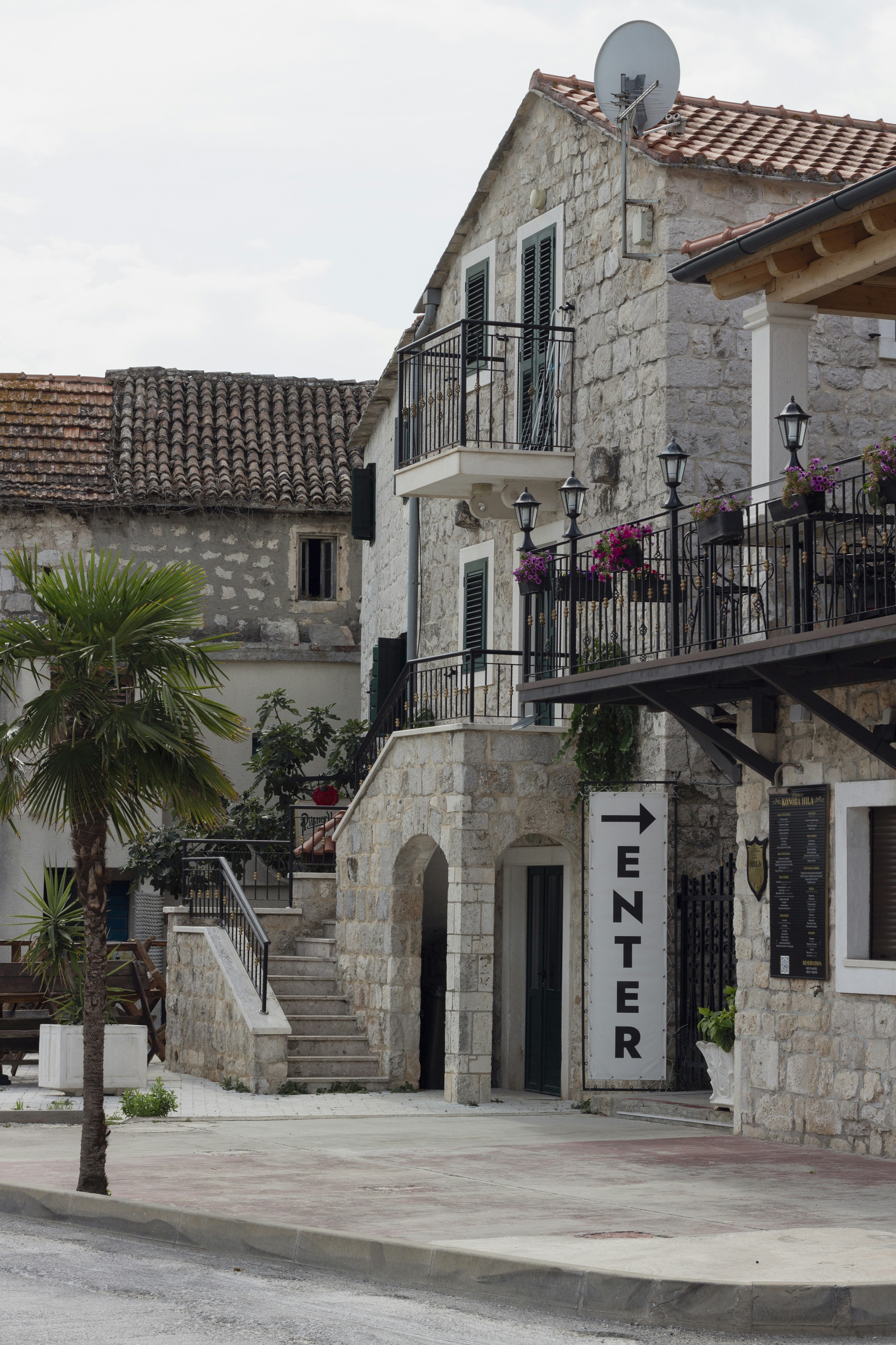 Enter Here: Sunlit Stone Facade with Balcony and Palm