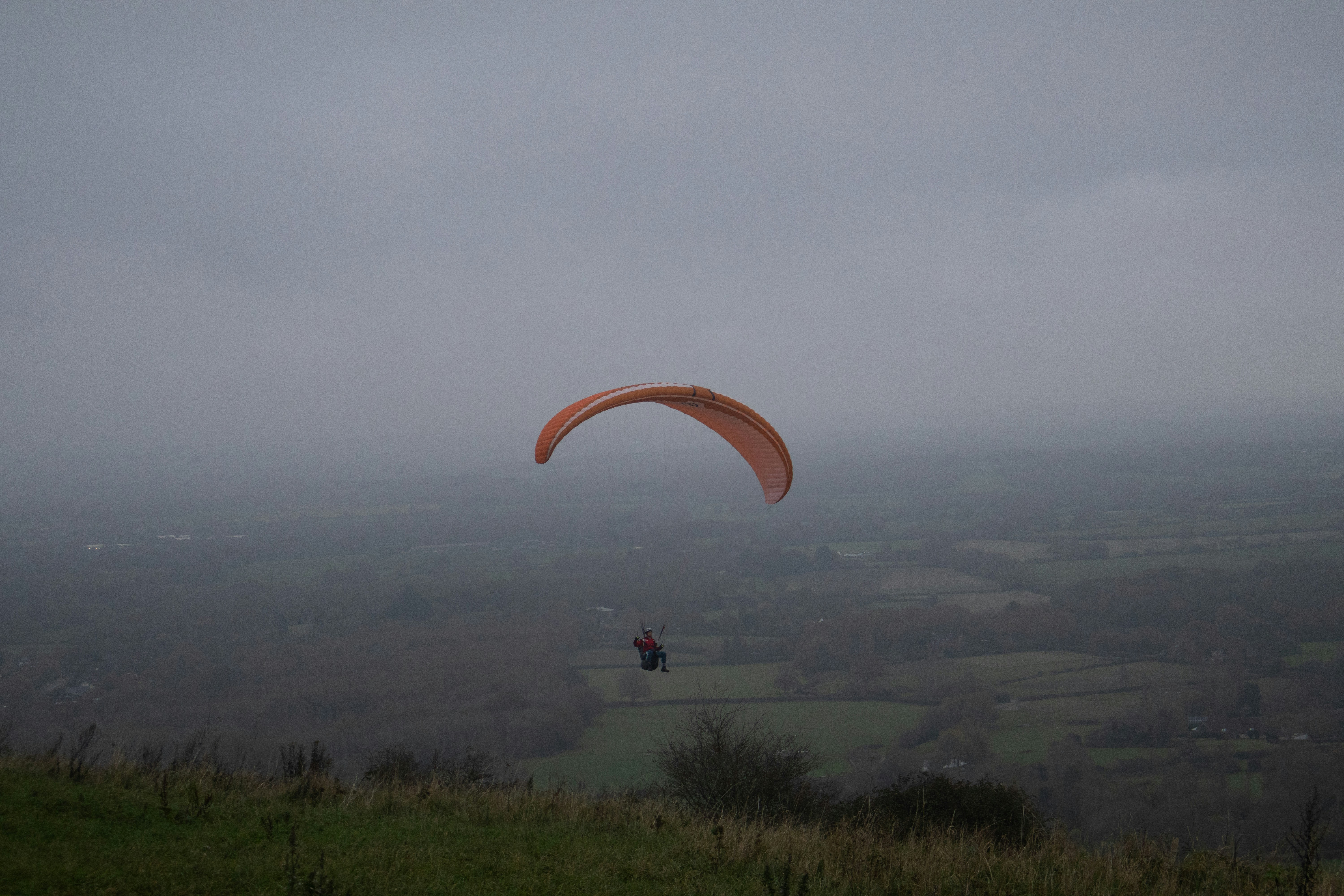 Amber Paraglider Tracing a Quiet Arc Over a Misty Countryside