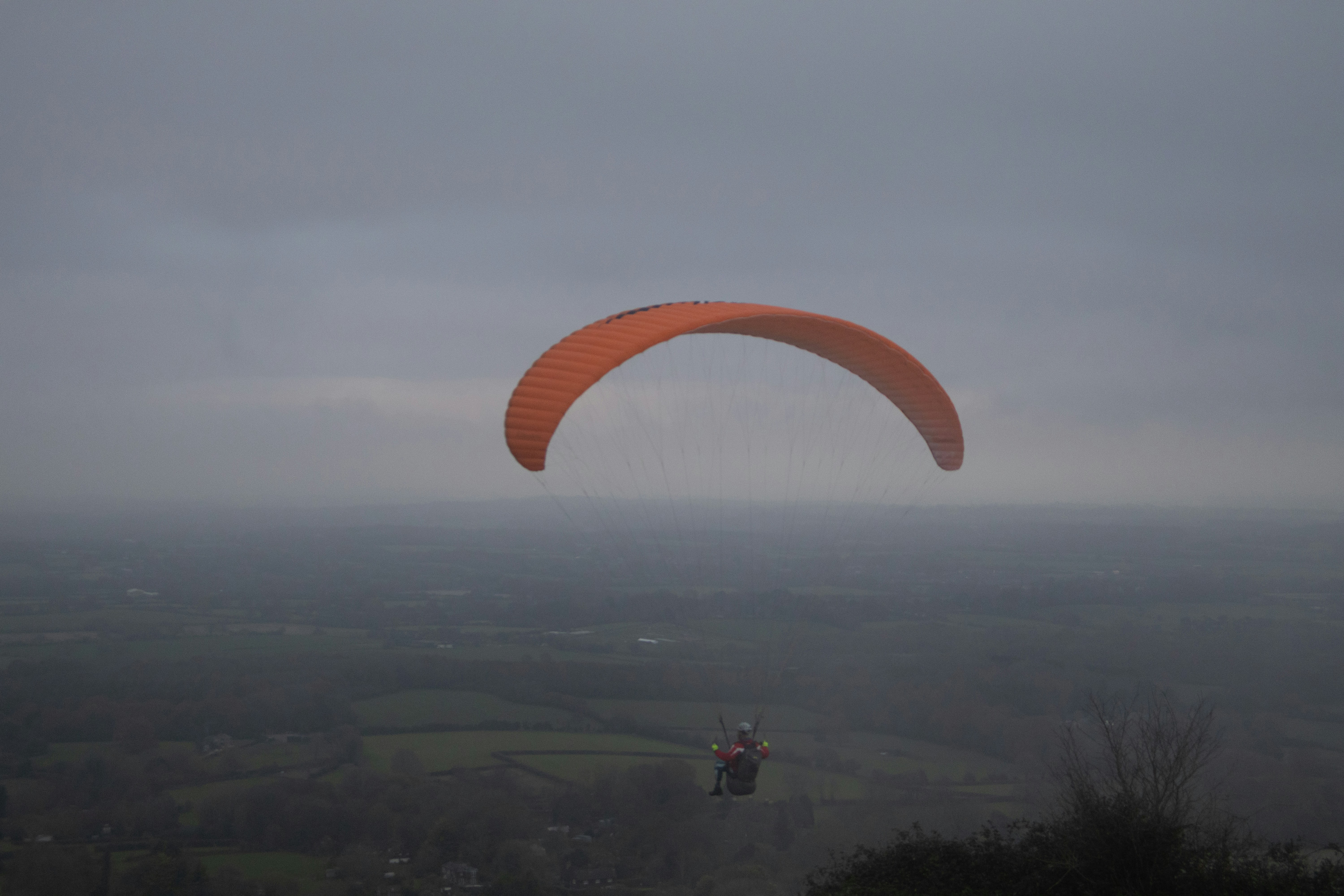 Crimson Arc Soaring Above a Patchwork Valley Under Clouded Skies