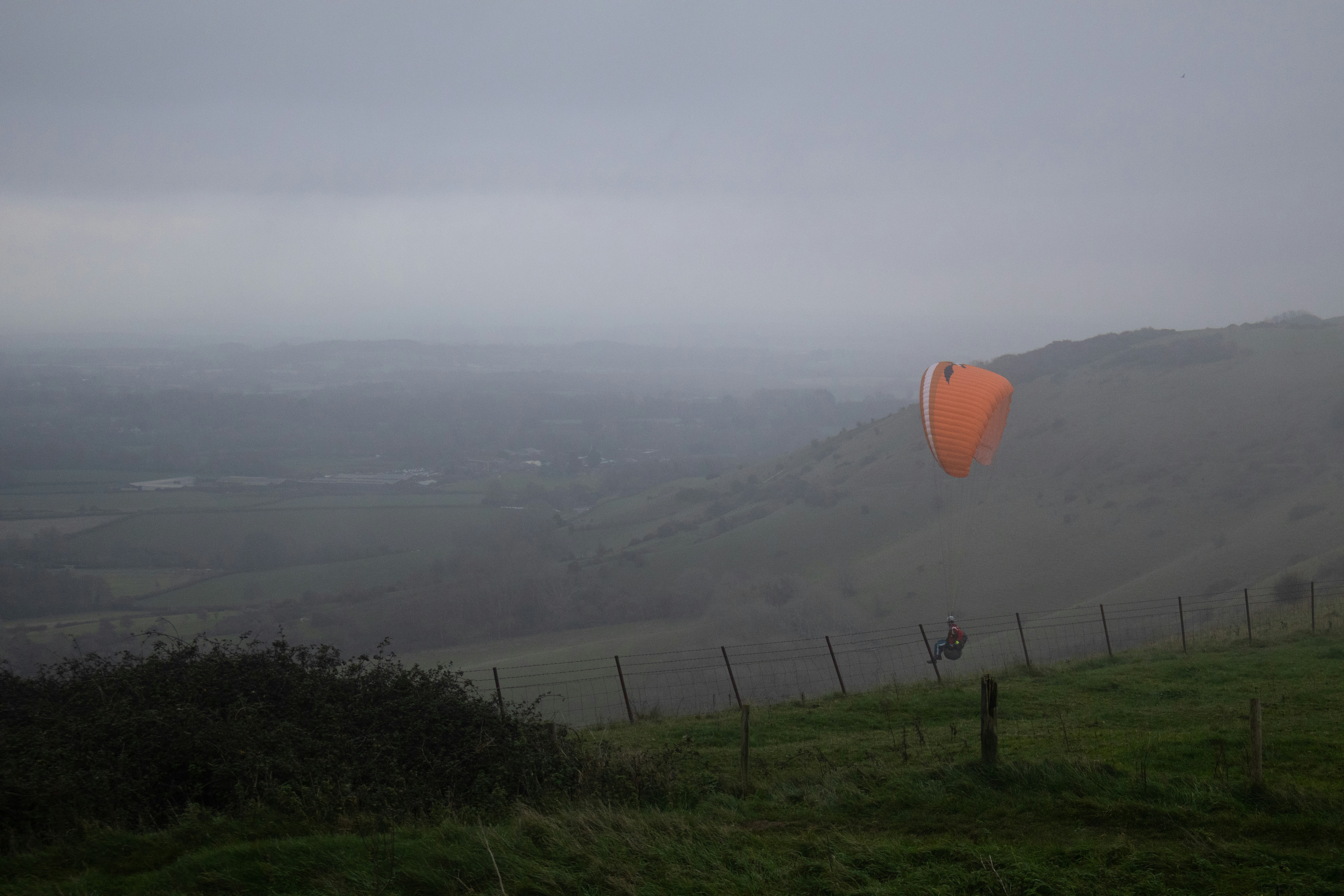Amber Paraglider Drifts Over a Misty Hillside