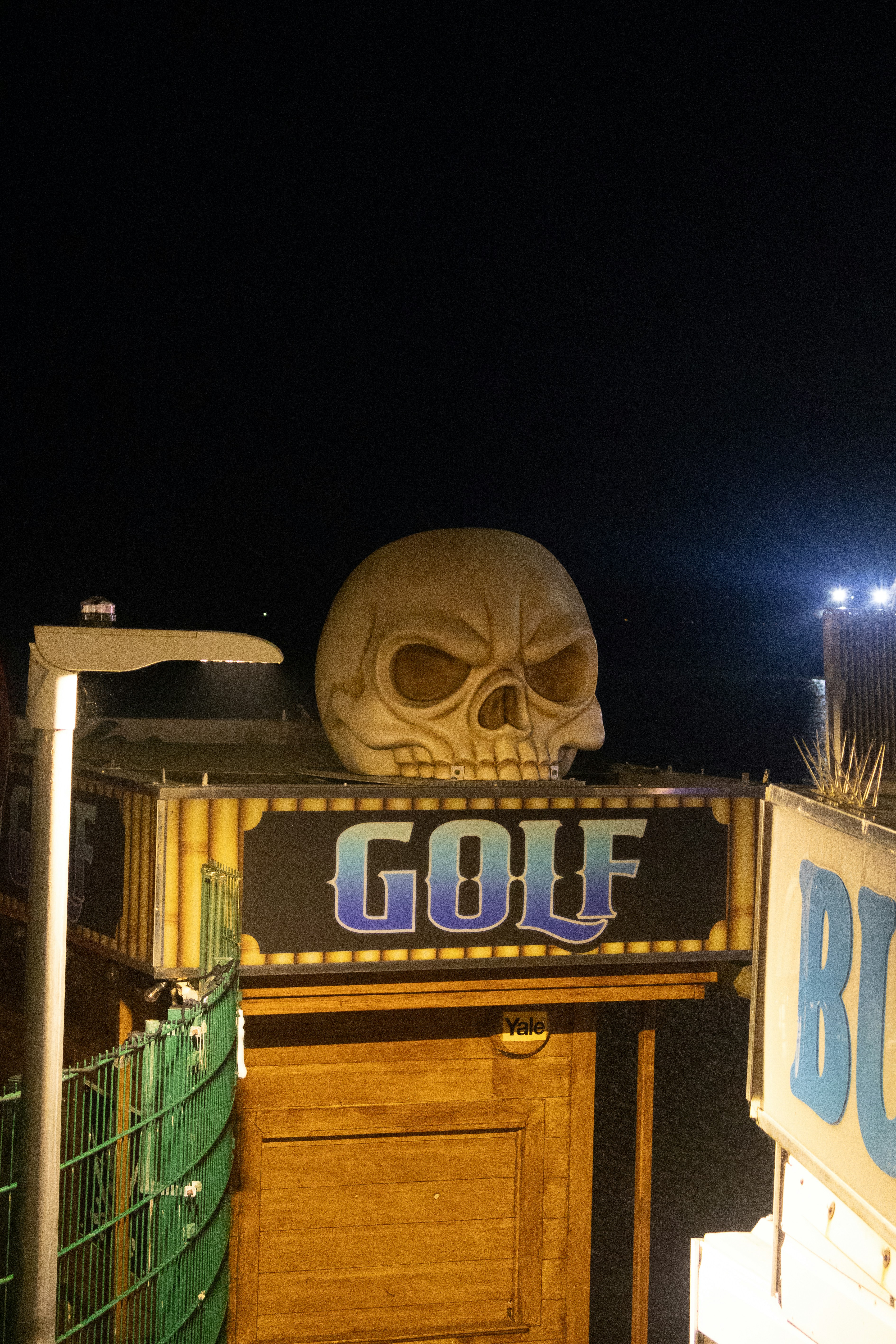 Night Sentinel Over the Mini-Golf Booth: Skull and Signage Under Streetlights