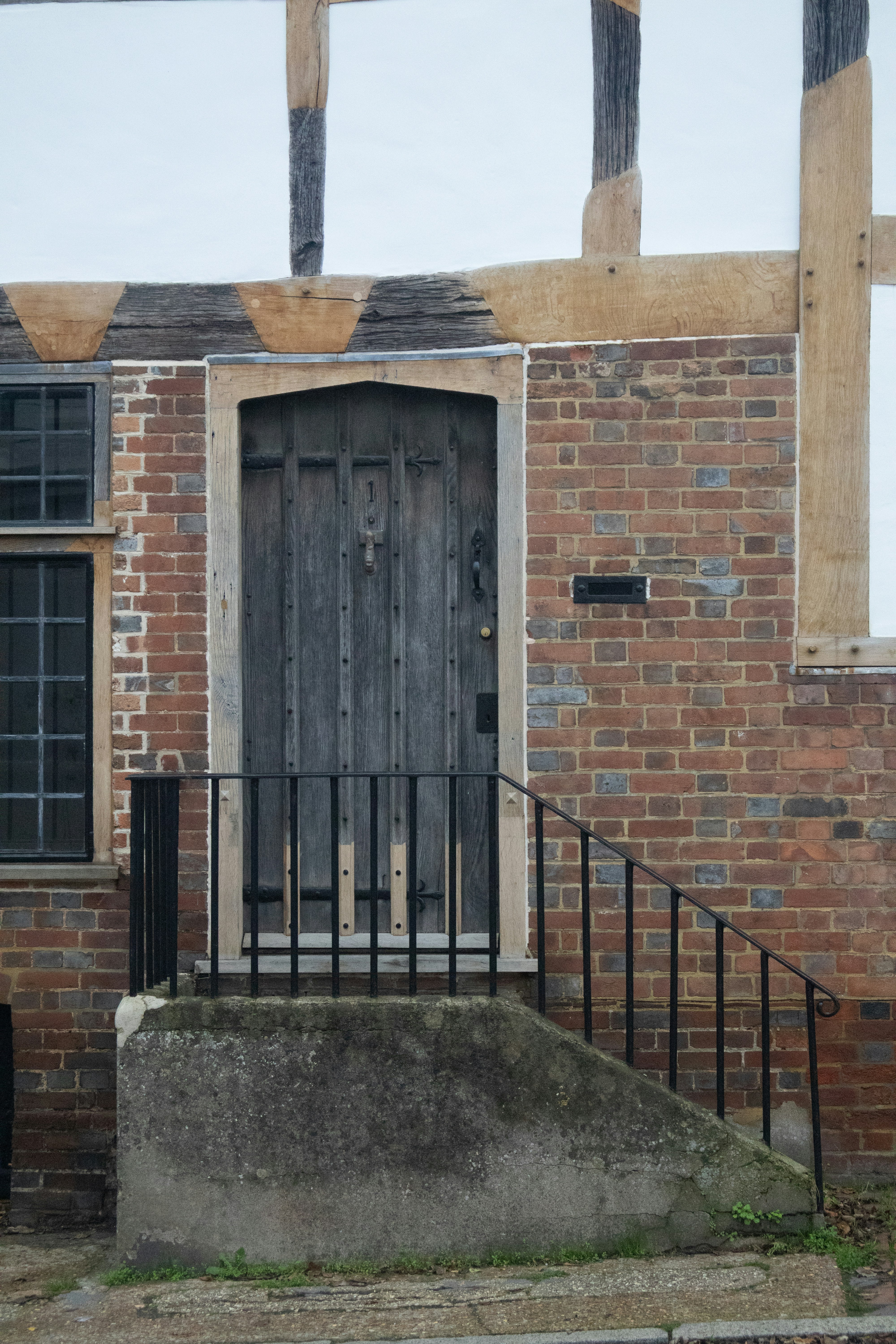 The Door of Time: A Quiet Brick Facade with Worn Timber and Iron Railings