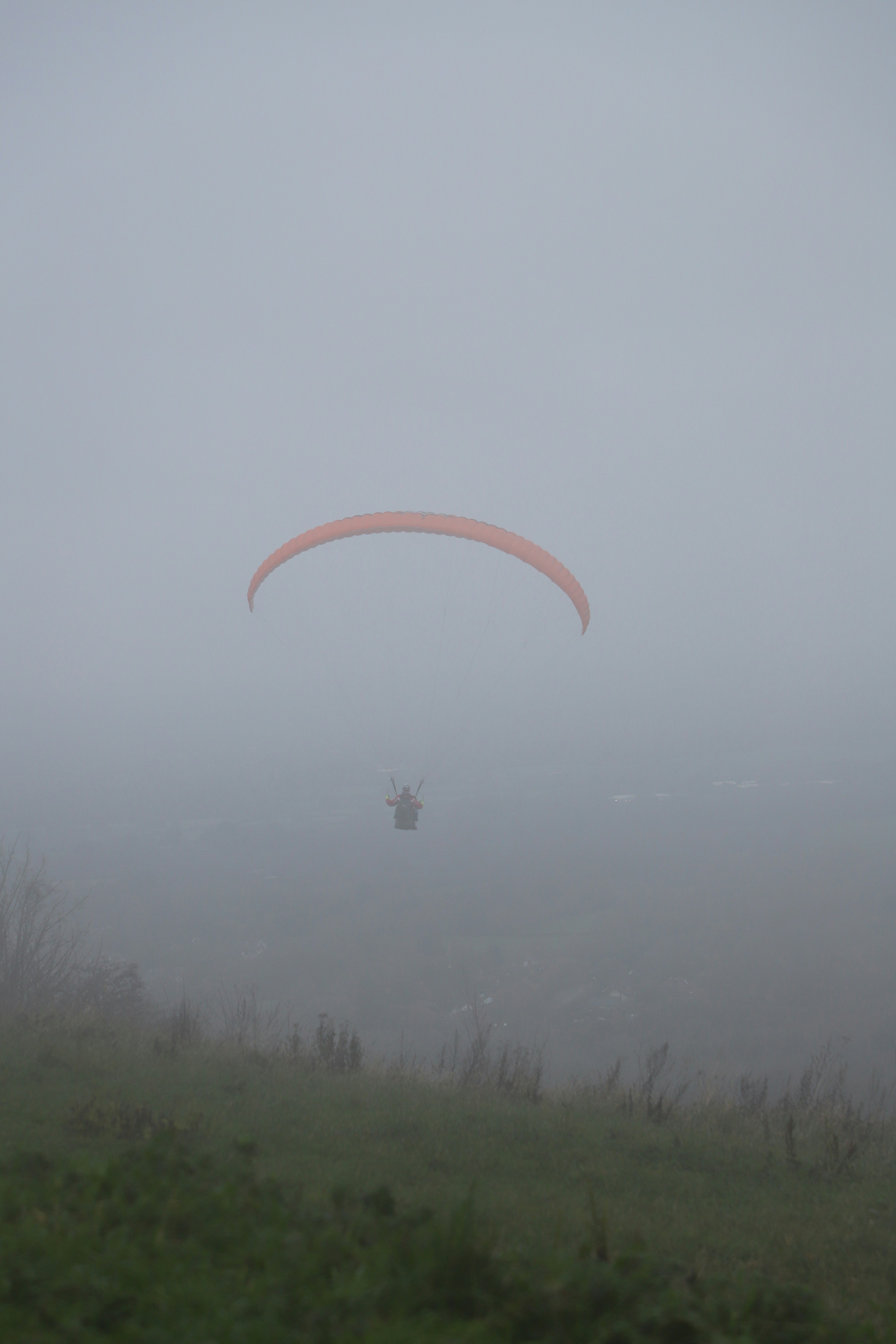 Red Arc in the Mist: Paraglider Hovering Over a Fogbound Valley
