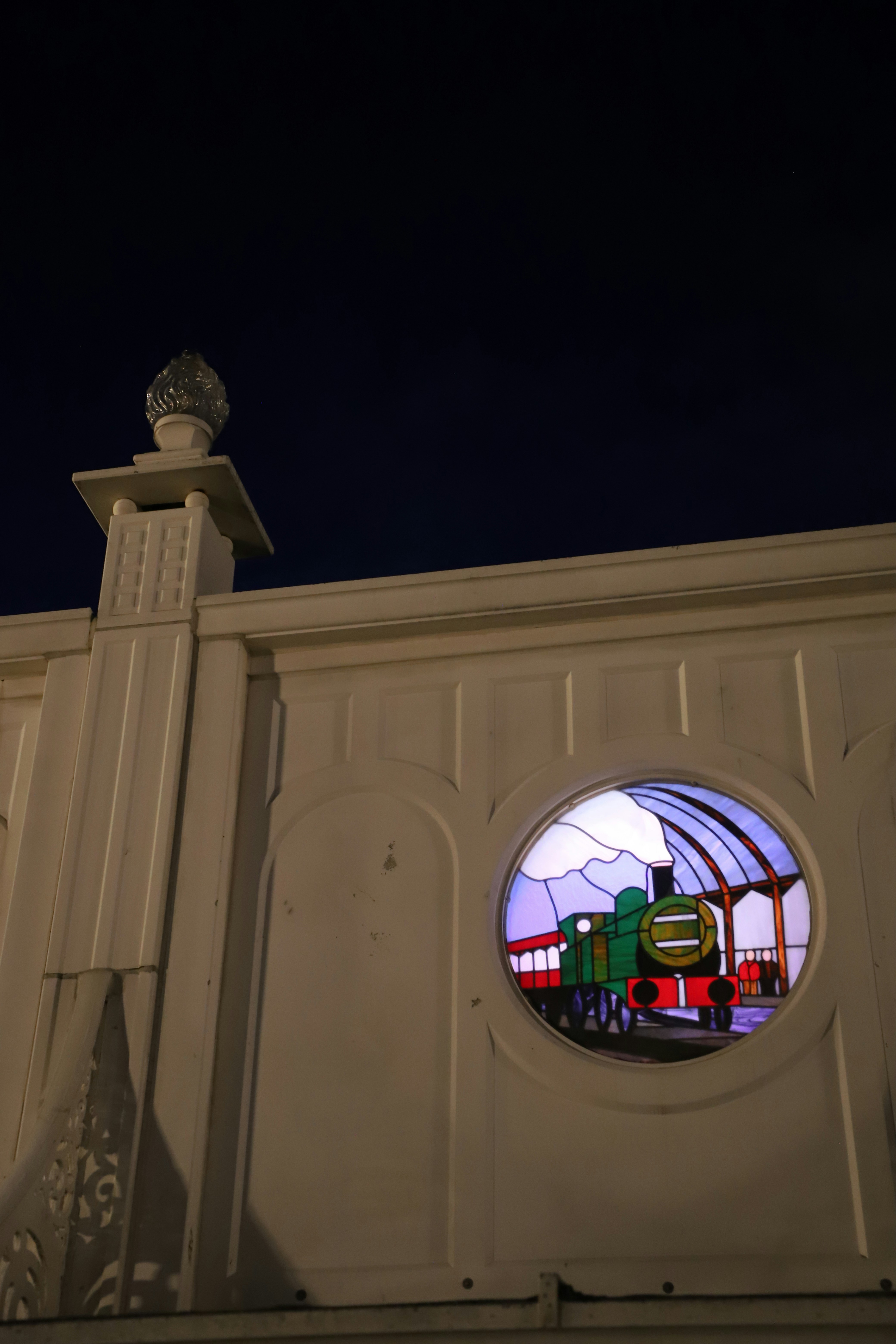 Circular stained-glass locomotive on a moonlit white wall