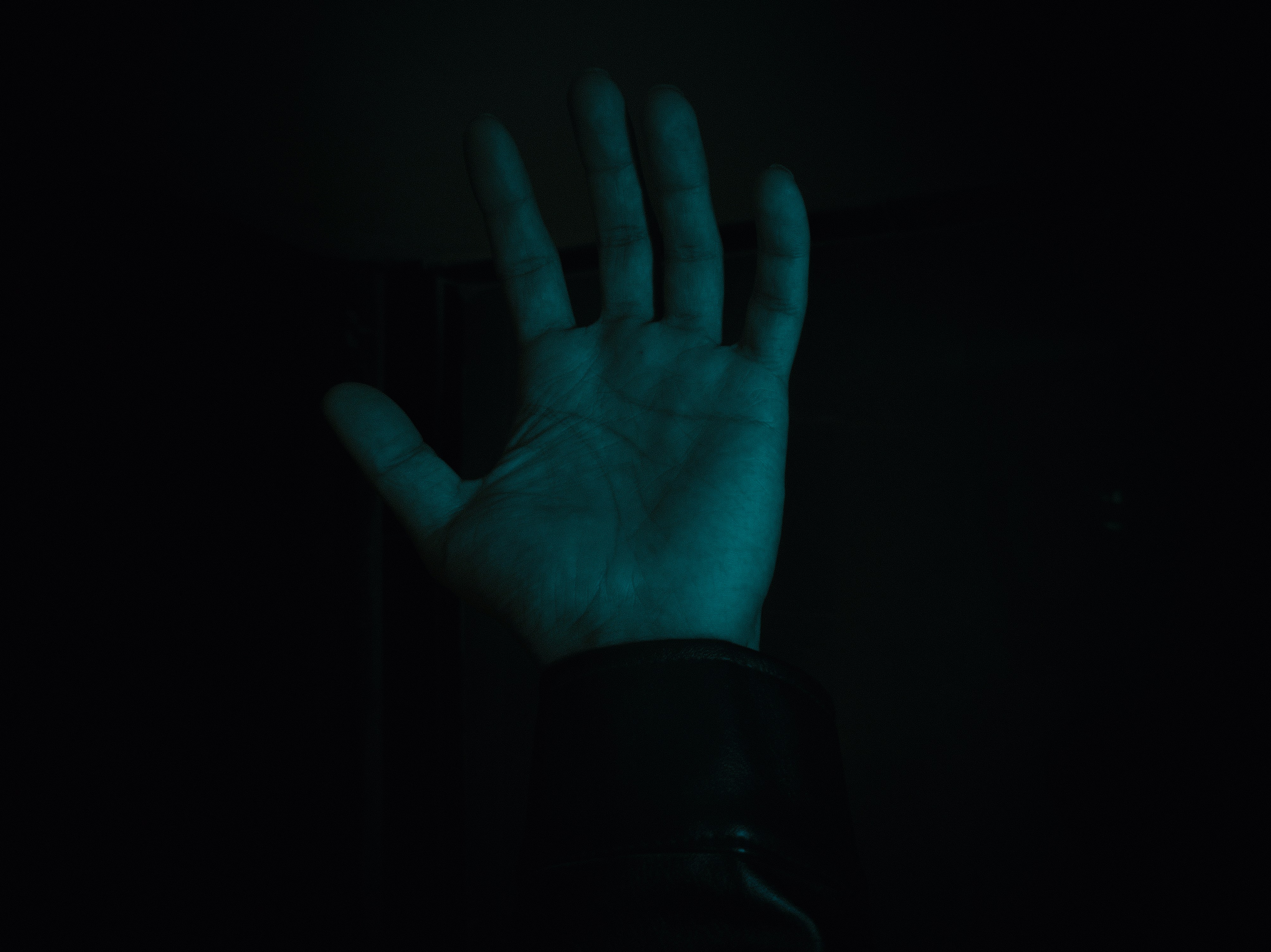 A hand illuminated by blue light against darkness