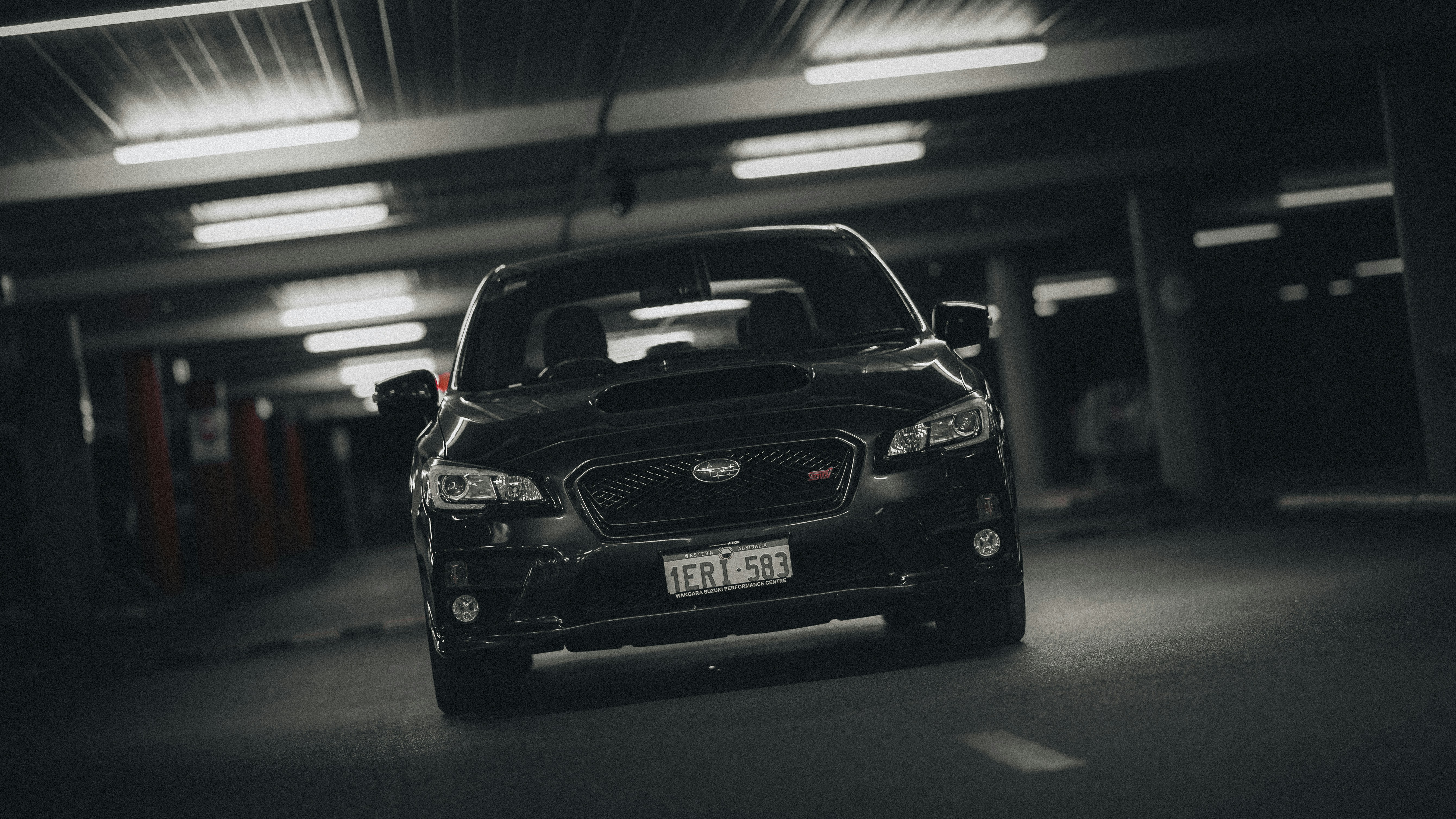 Under Neon Loom: Front-Facing Black Sedan in an Empty Parking Garage