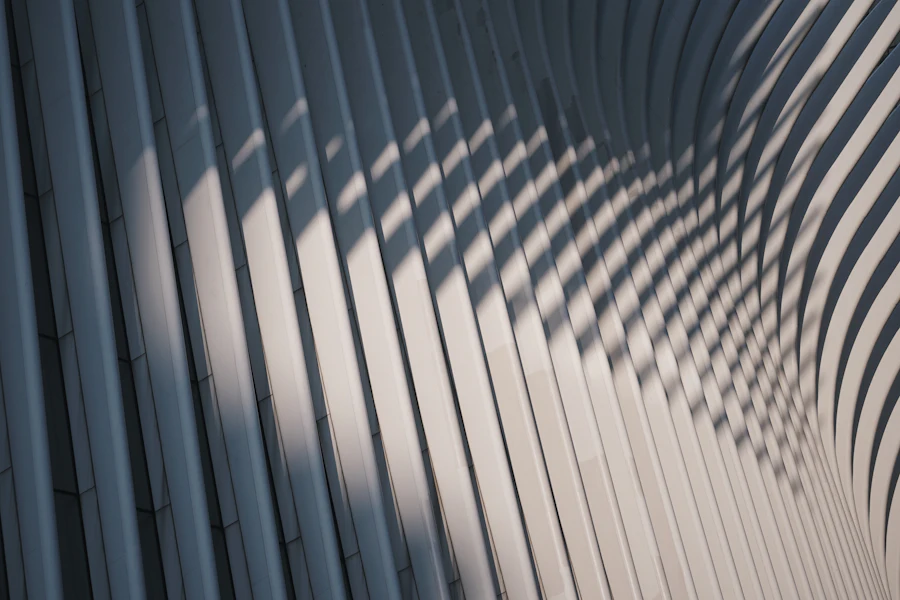 Sweeping architectural facade with repeating vertical fins and a lattice of diagonal shadows across a bright curved wall.