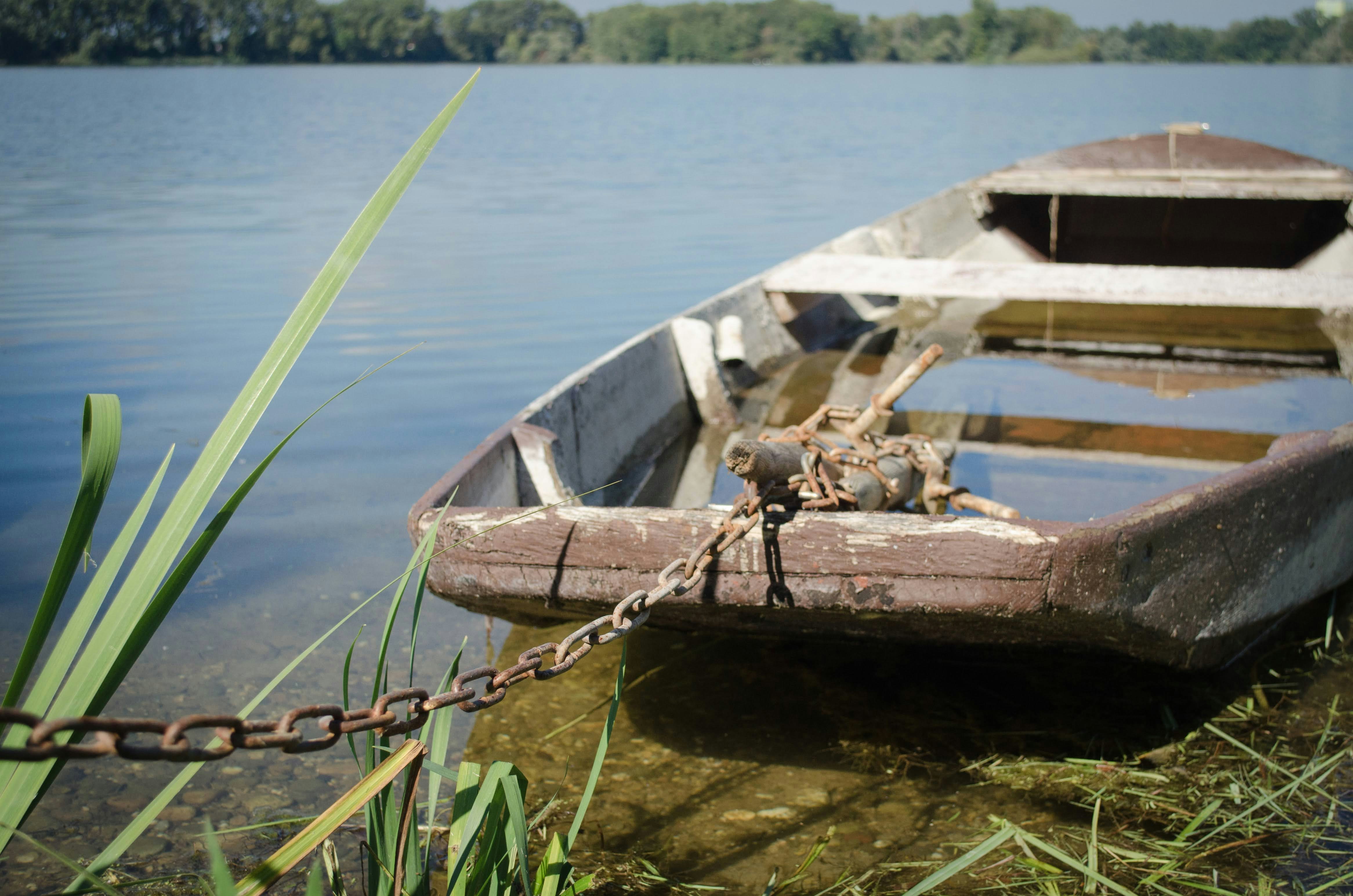 Weathered Rowboat Anchored by a Crooked Chain on a Quiet Lake