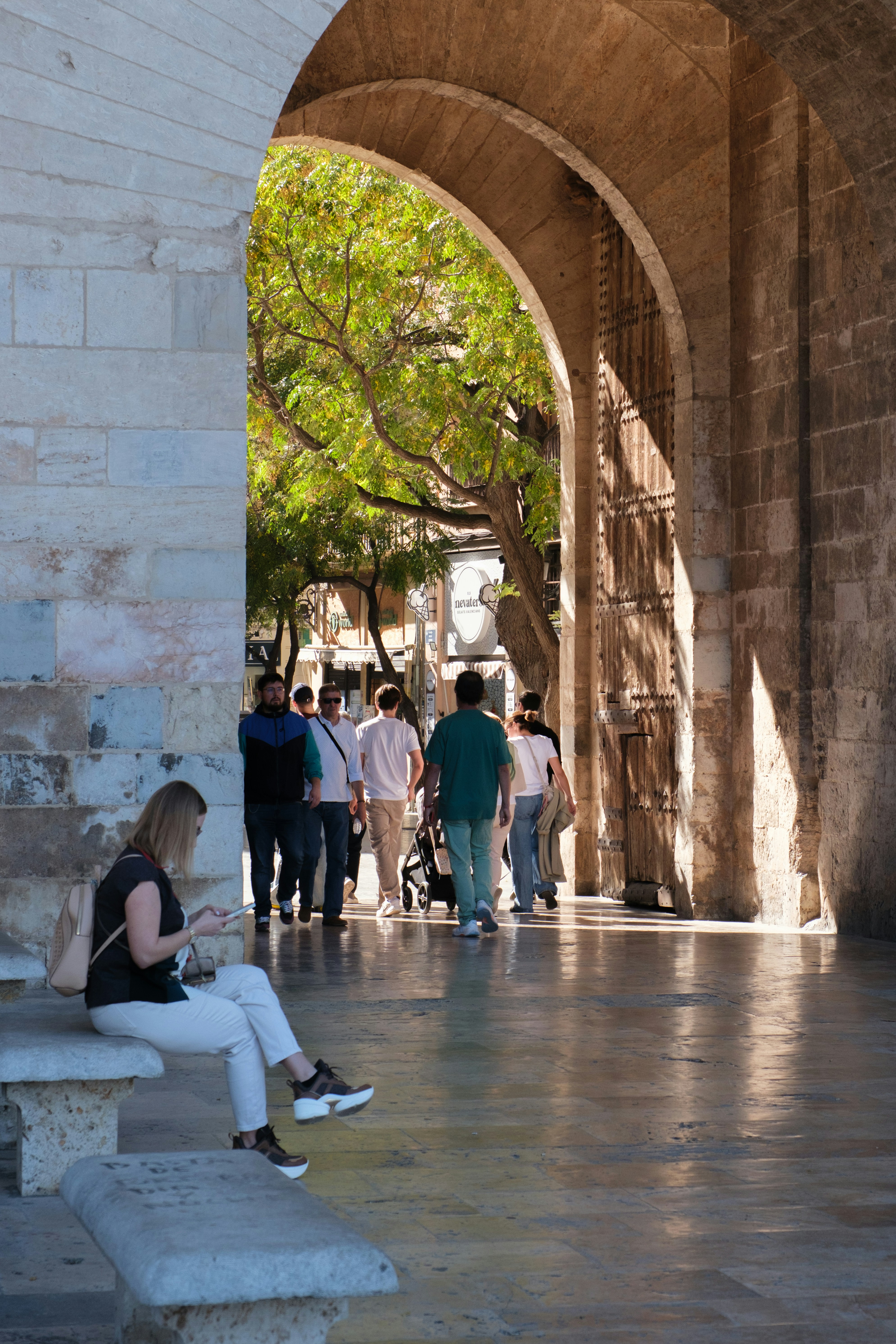 Sunlit Archway Crossing: Crowds Move Through Timeworn Stone