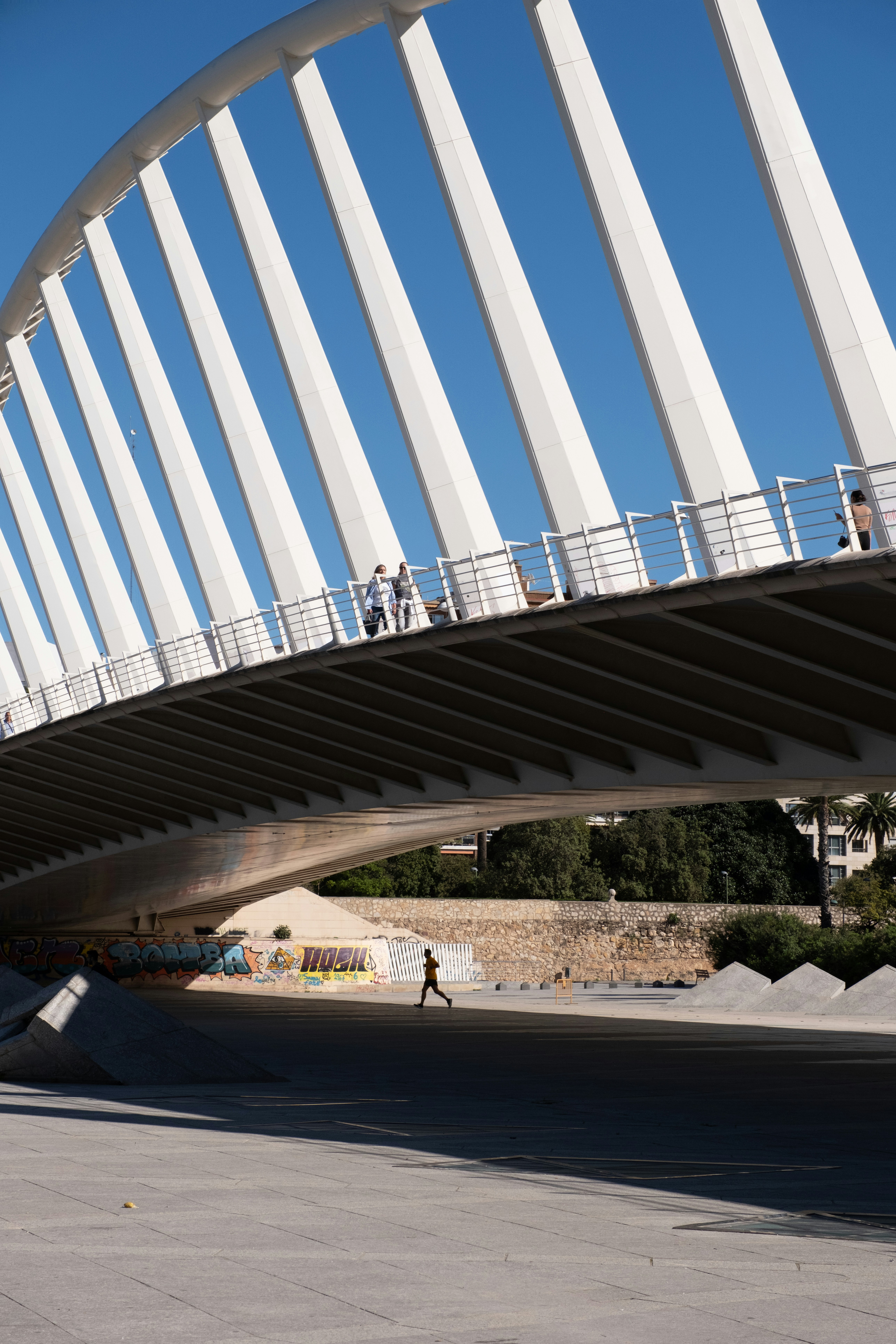 Sunlit Ribs: Pedestrians on a White-Arch Bridge