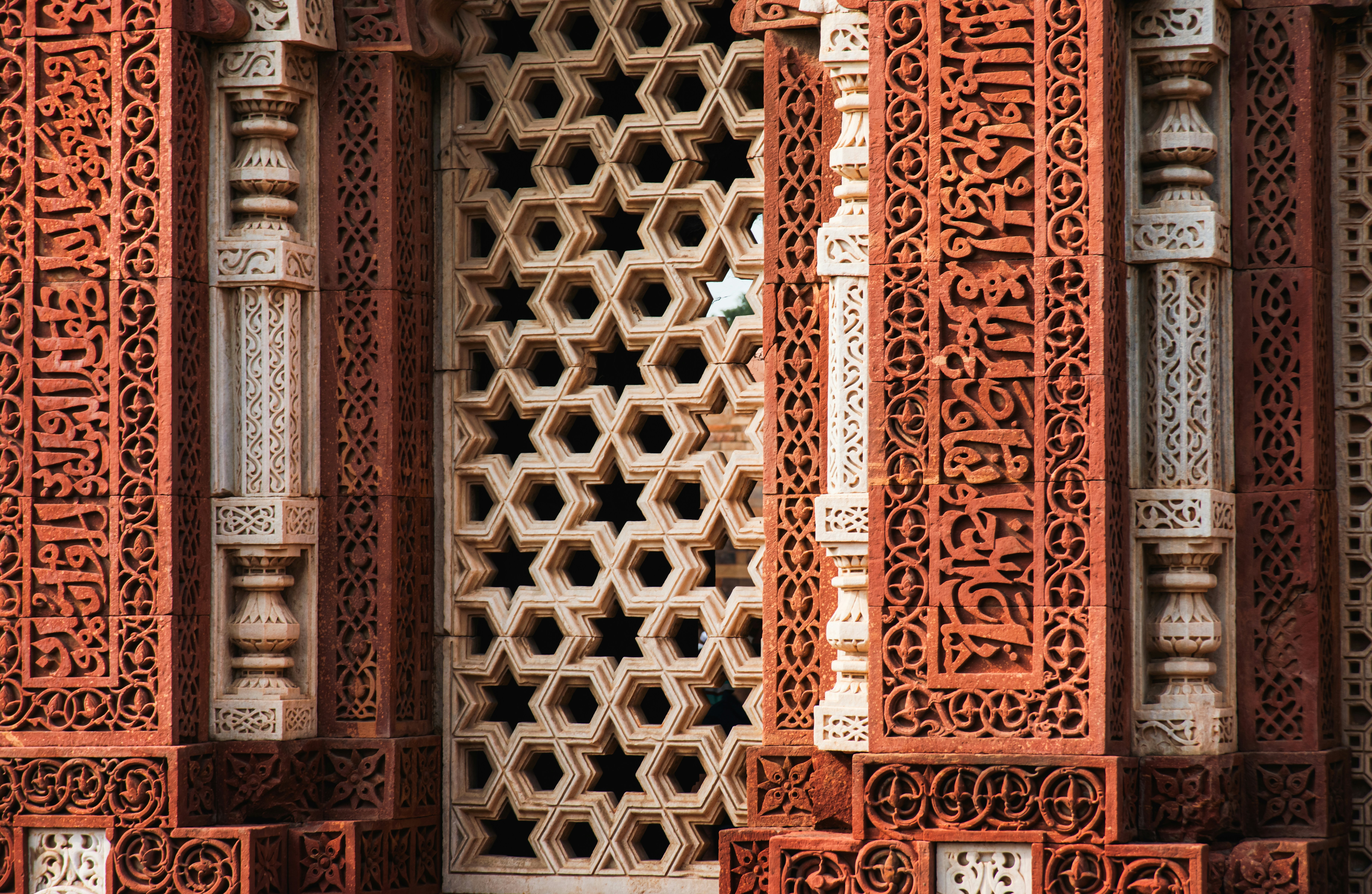 A close view of the carved stone jali window of Alai Darwaza in the Qutb Minar complex. Photographed from the exterior, it highlights dense Arabic calligraphy, floral motifs, and geometric stonework that reflect early Indo Islamic craftsmanship. The lattice features the characteristic star shaped pattern seen across Sultanate era monuments.