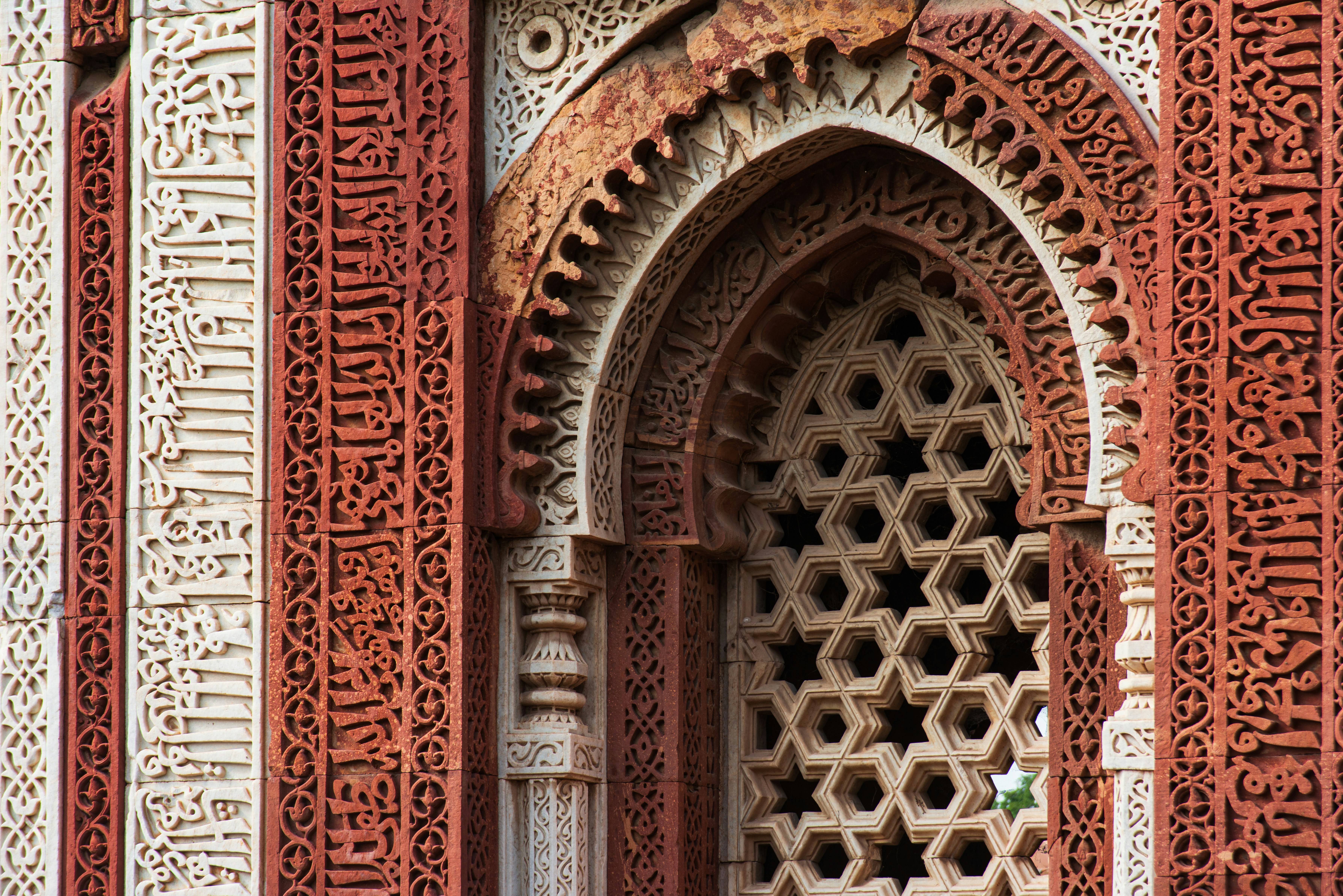 A close view of the carved stone jali window of Alai Darwaza in the Qutb Minar complex. Photographed from the exterior, it highlights dense Arabic calligraphy, floral motifs, and geometric stonework that reflect early Indo Islamic craftsmanship. The lattice features the characteristic star shaped pattern seen across Sultanate era monuments.