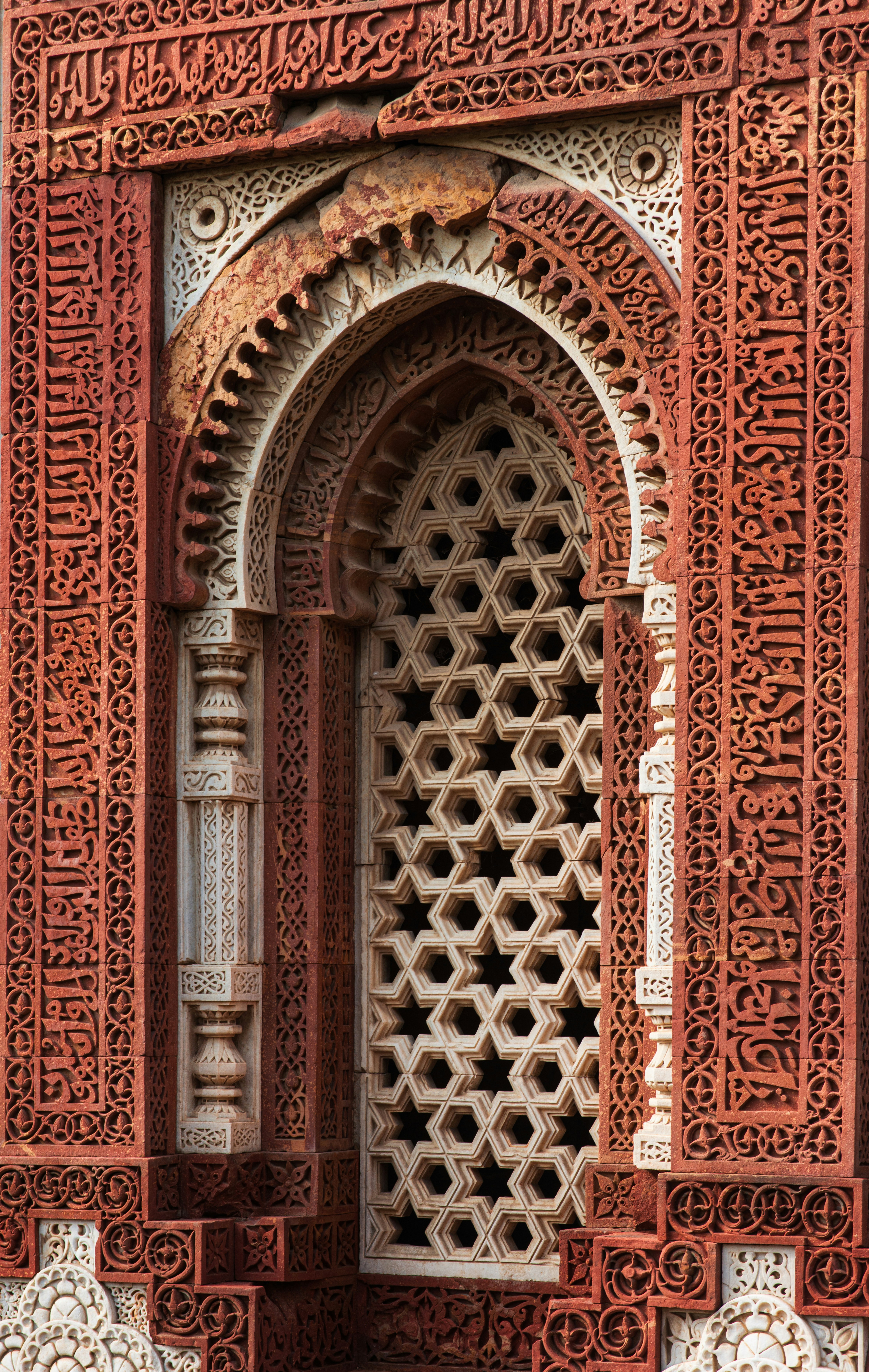A close view of the carved stone jali window of Alai Darwaza in the Qutb Minar complex. Photographed from the exterior, it highlights dense Arabic calligraphy, floral motifs, and geometric stonework that reflect early Indo Islamic craftsmanship. The lattice features the characteristic star shaped pattern seen across Sultanate era monuments.