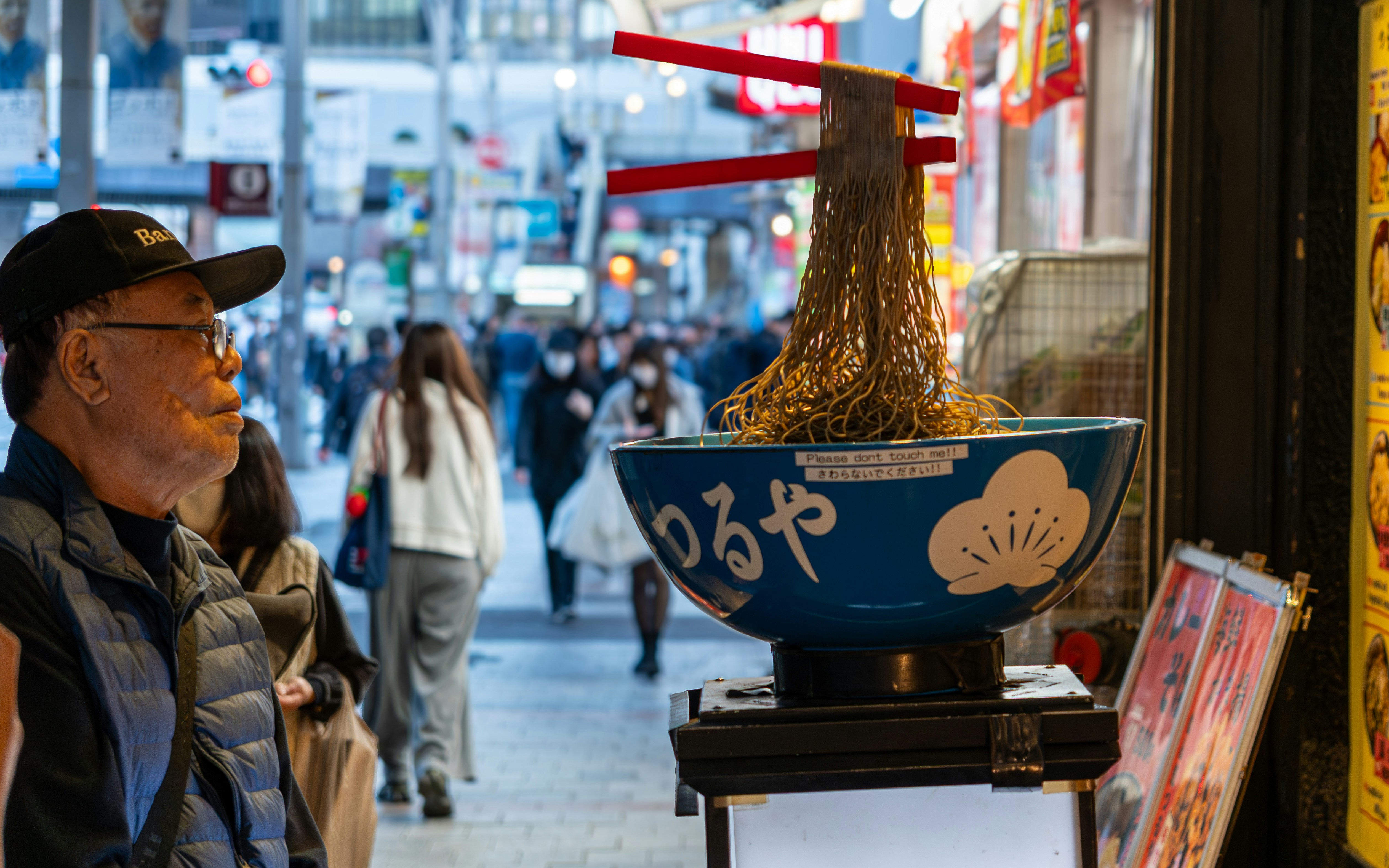 A surreal street-scene moment featuring a giant floating noodle bowl display catching the attention of a passerby. The backdrop of a busy city street adds an energetic contrast to the whimsical installation. A playful blend of street photography, culture, and visual storytelling.