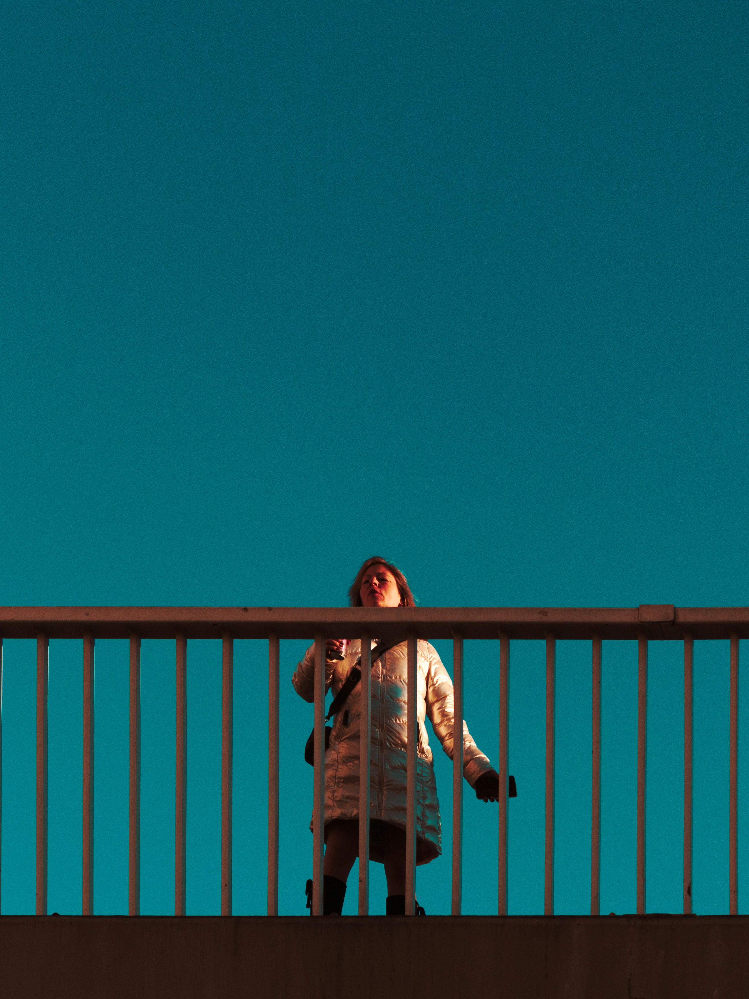 Edge of Quiet: A Figure Framed by Railings Under a Teal Sky