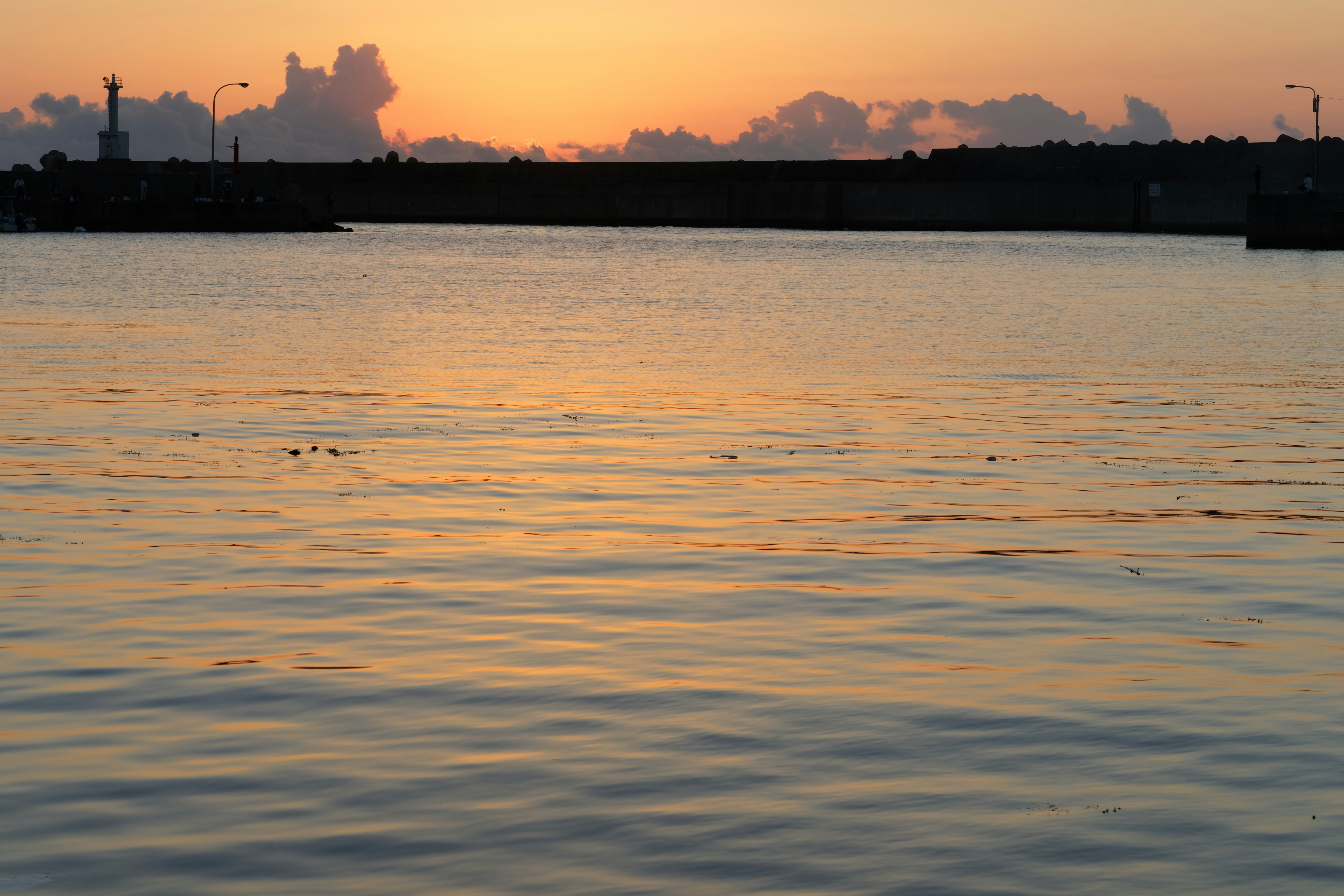 Sunset over a calm harbor with lighthouse.
