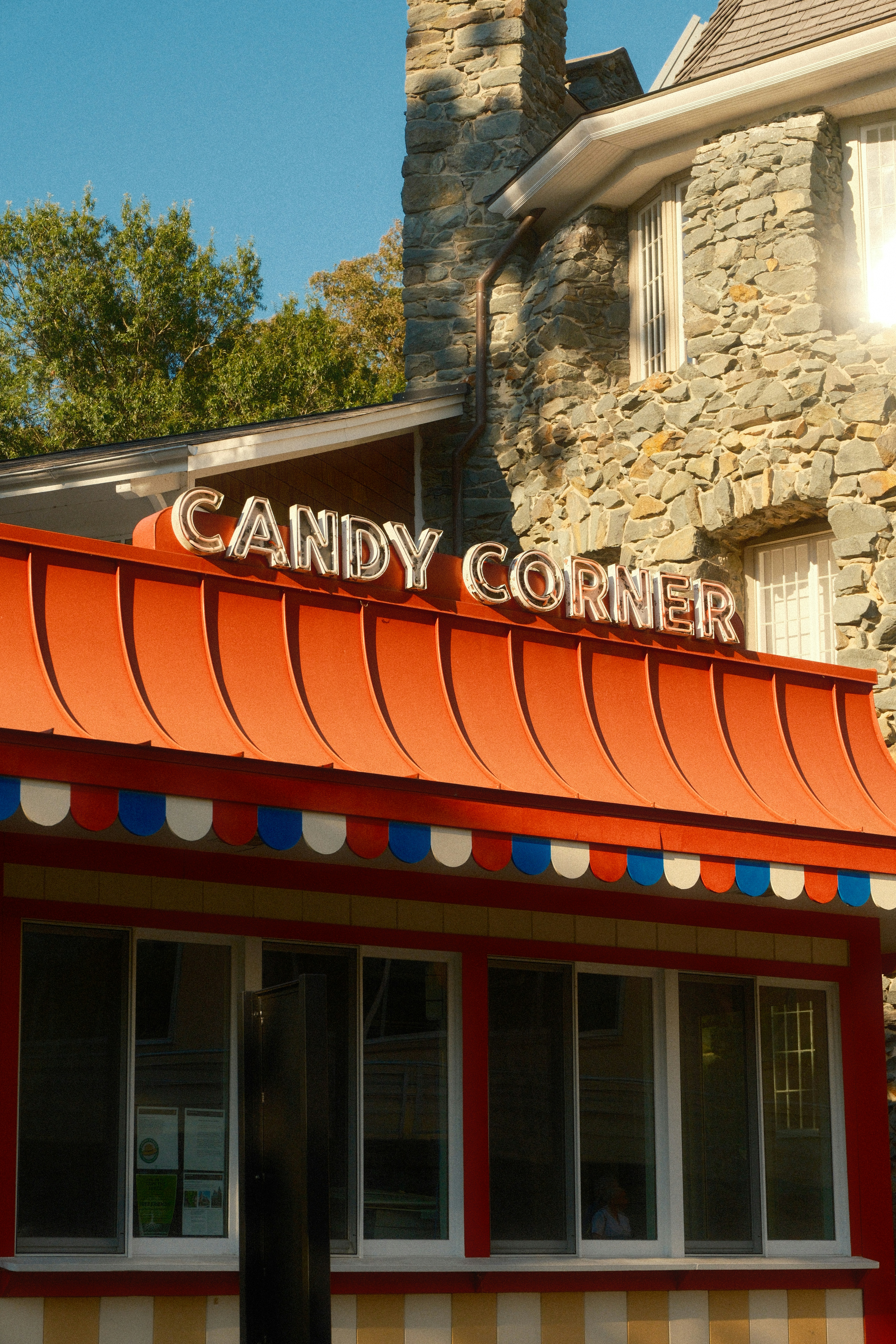 Candy Corner: Sunlit Red Awning Over a Stone-Shopfront