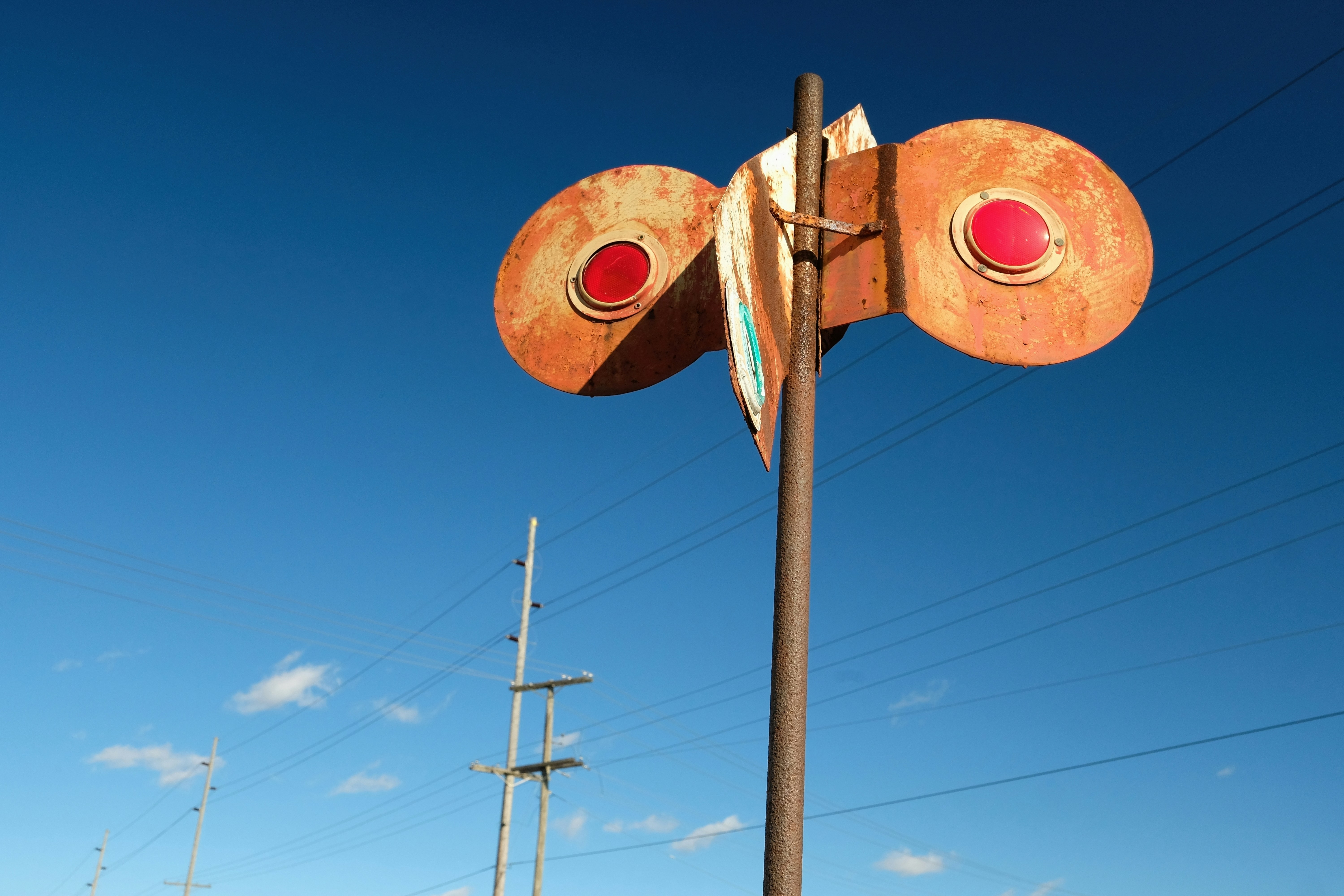 An old railroad sign stands weathered against a blue sky and telephone wires.