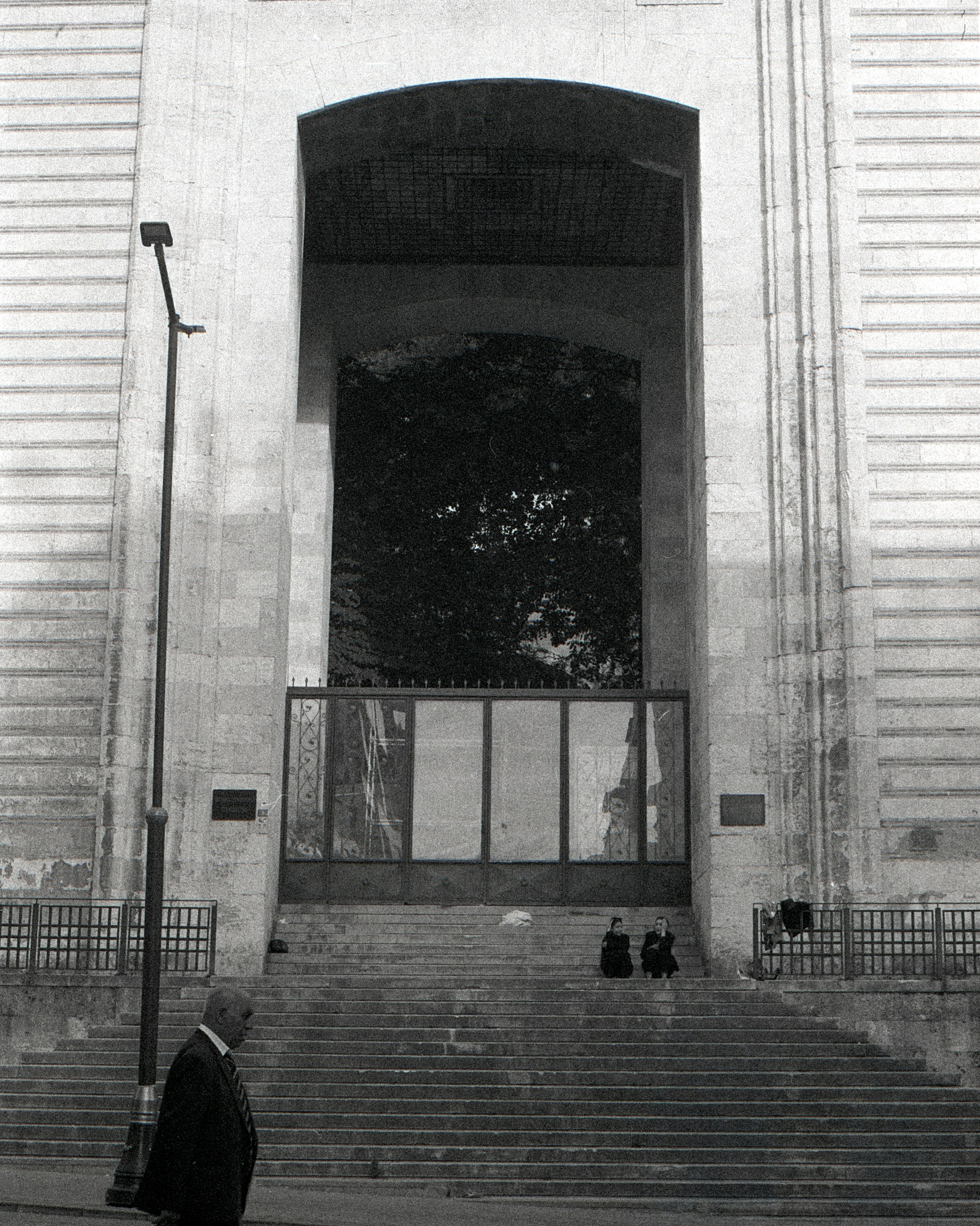 People walking up steps towards a large arched entrance.