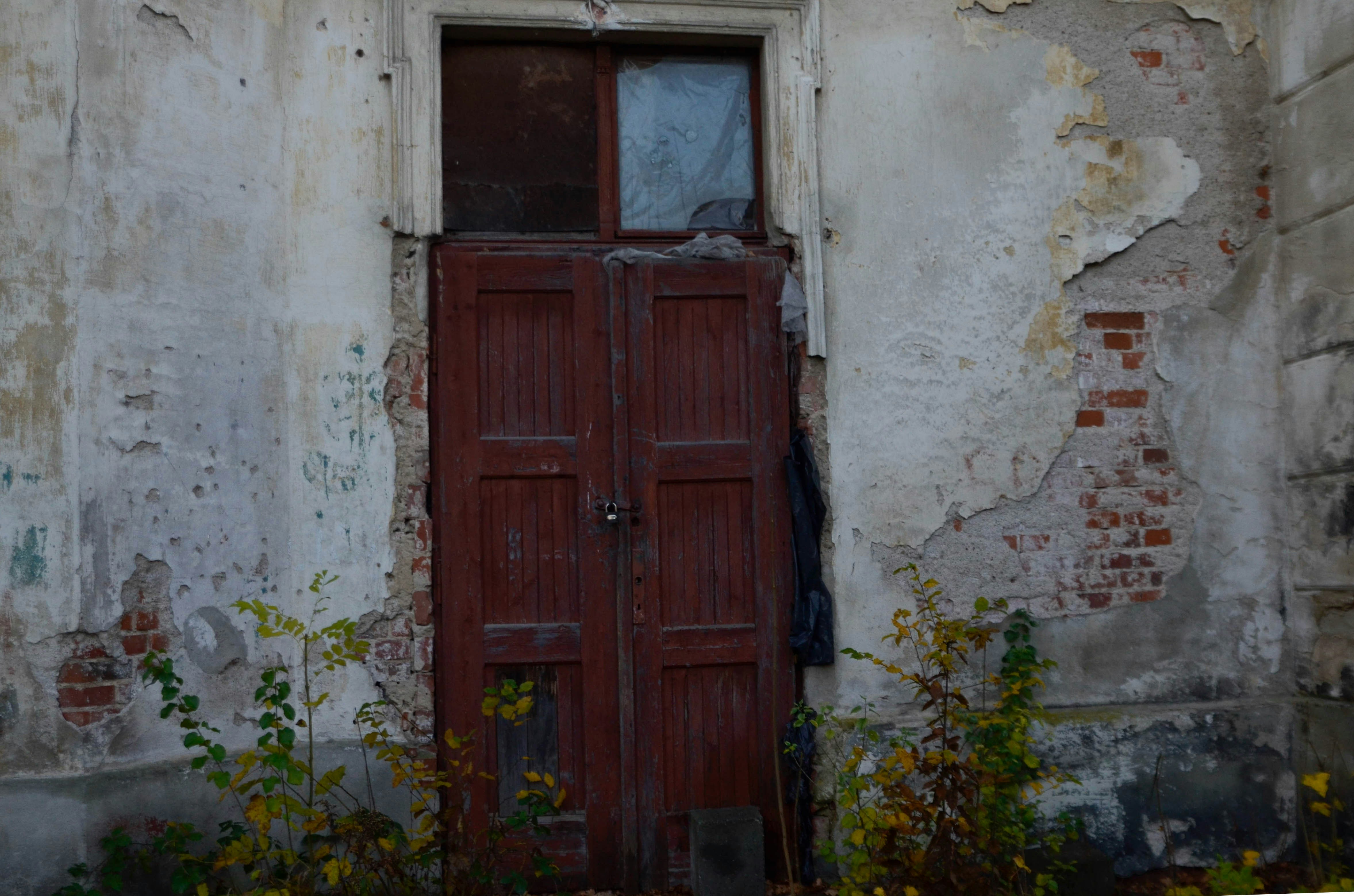 Weathered Doorway: A Rust-Red Entry Framed by Crumbling Plaster
