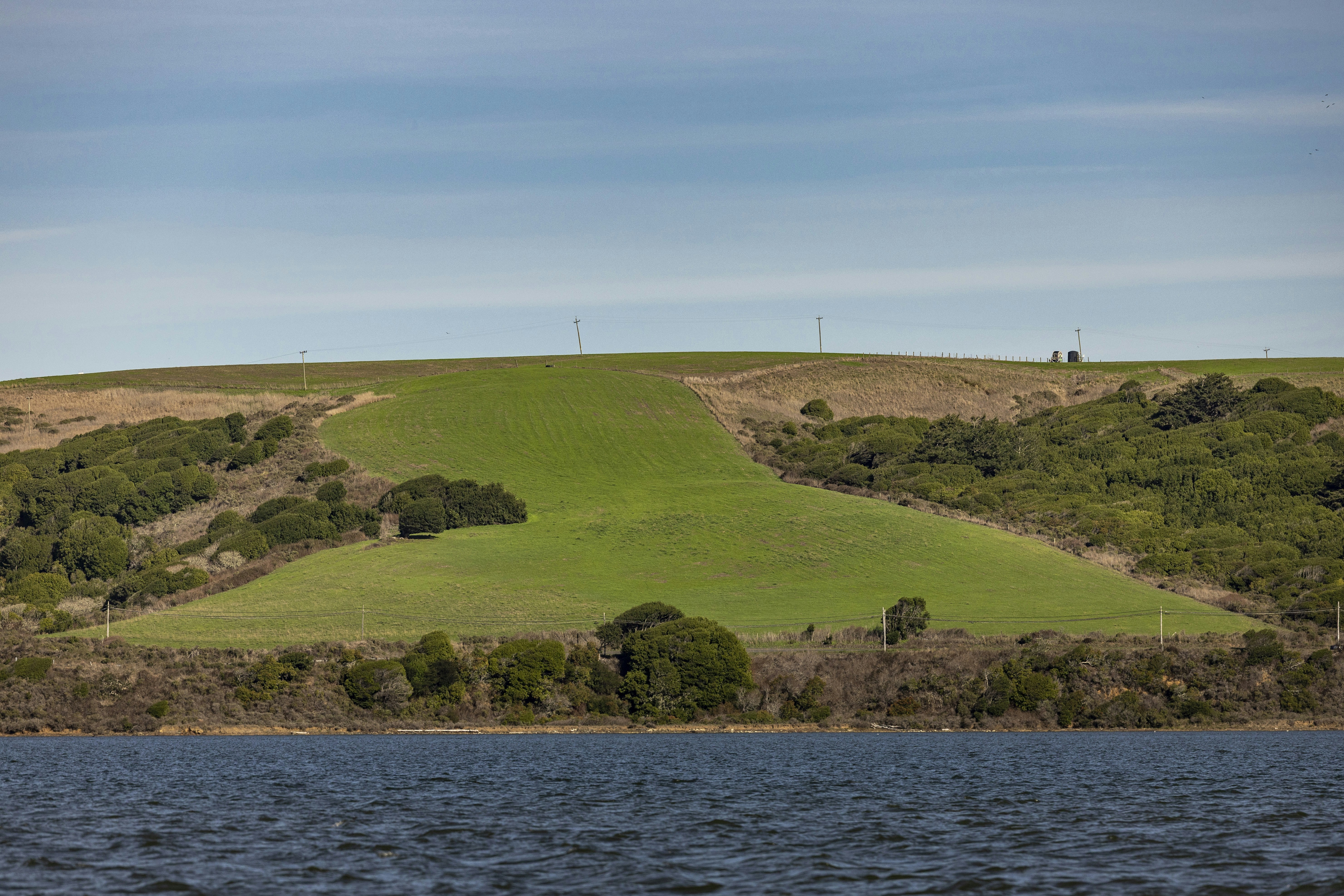 Green Crest Over Blue Water: A Quiet Hillscape Under an Expansive Sky
