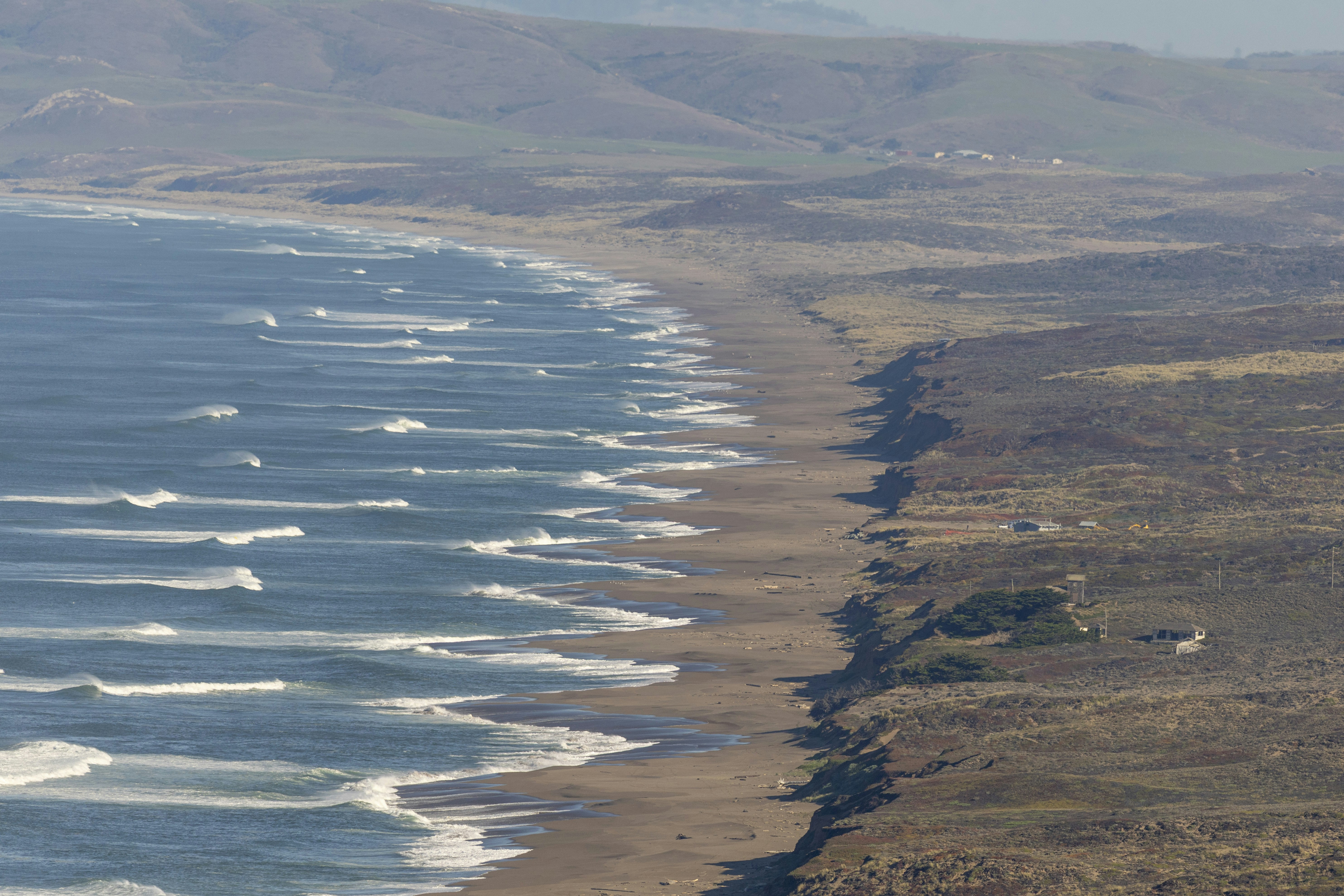 Ocean waves crash on a sandy beach with rolling hills.