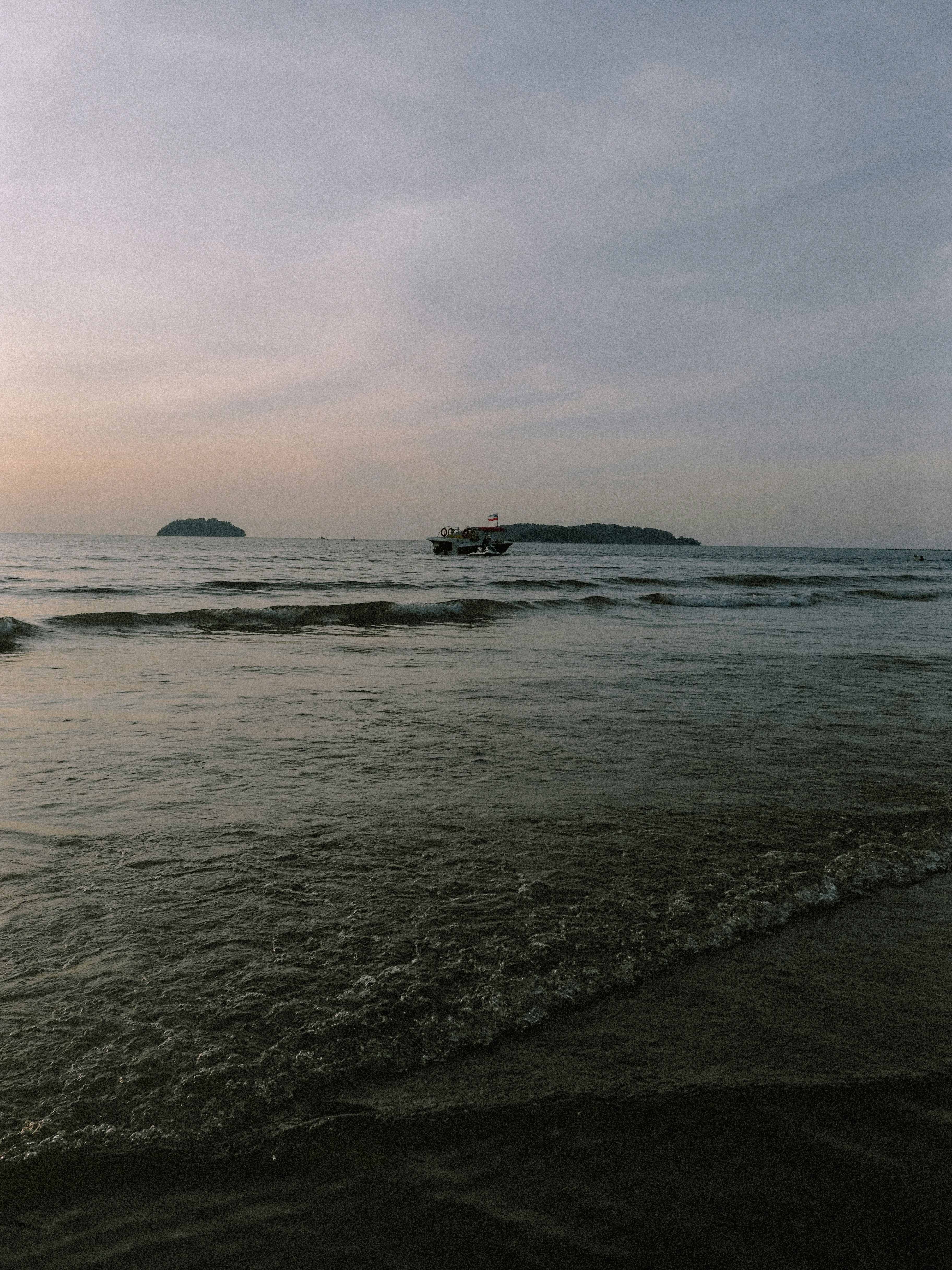 Waves lap the shore with islands in the distance.