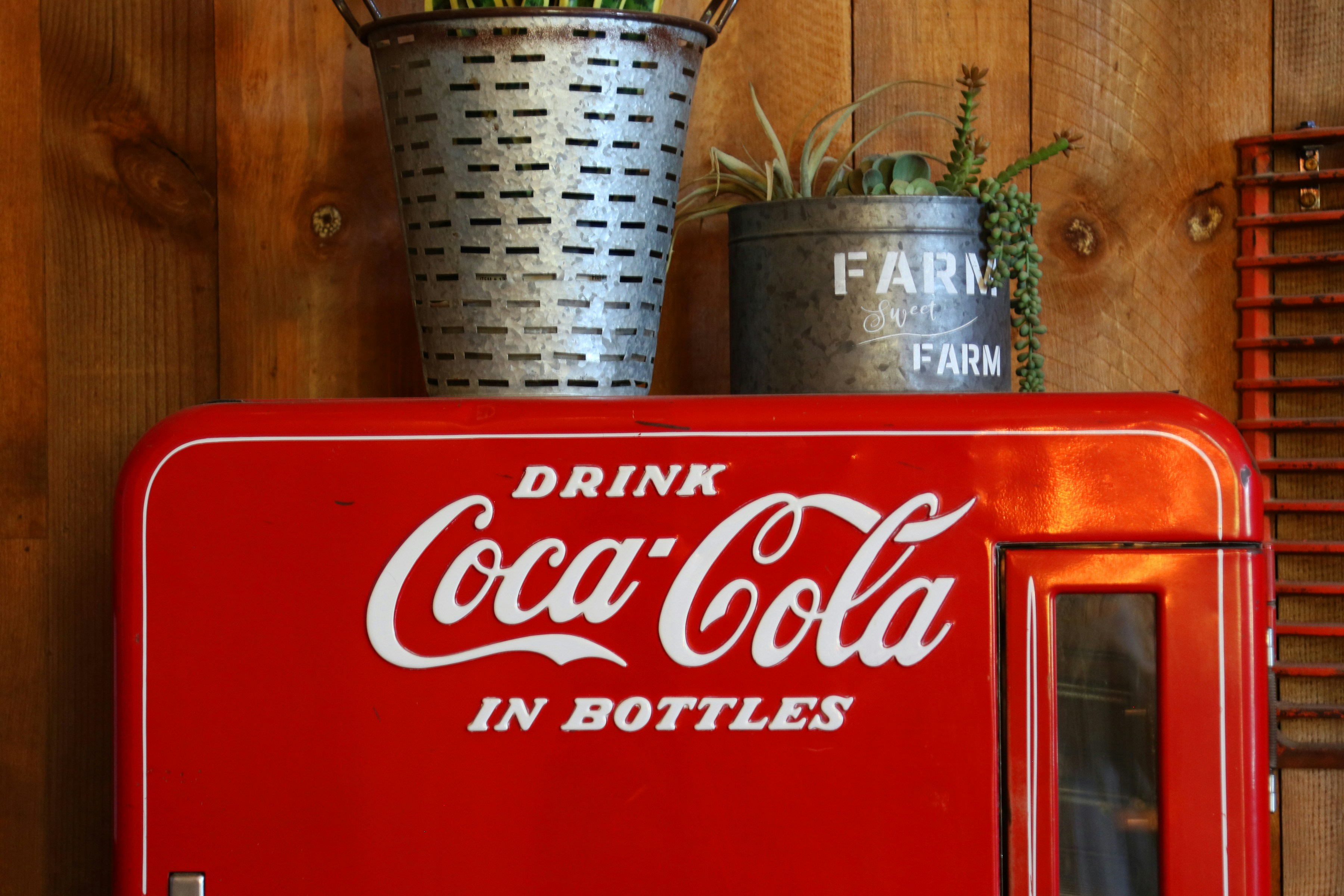 Crimson Centerpiece: A Retro Coca-Cola Fridge Framed by Rustic Farm Pots