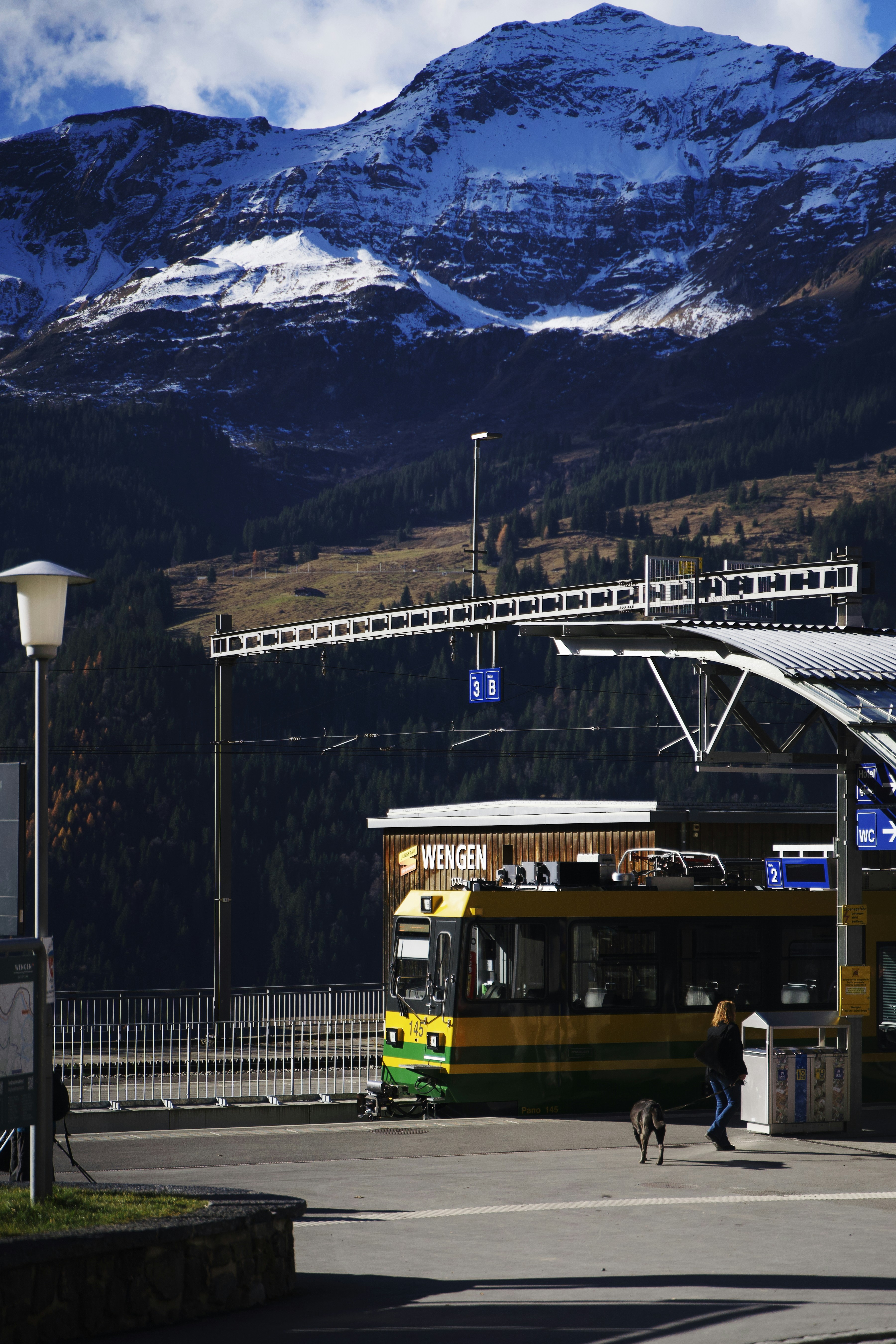 Wengen Stopover: Yellow-Green Tram at the Foot of Snowy Alps