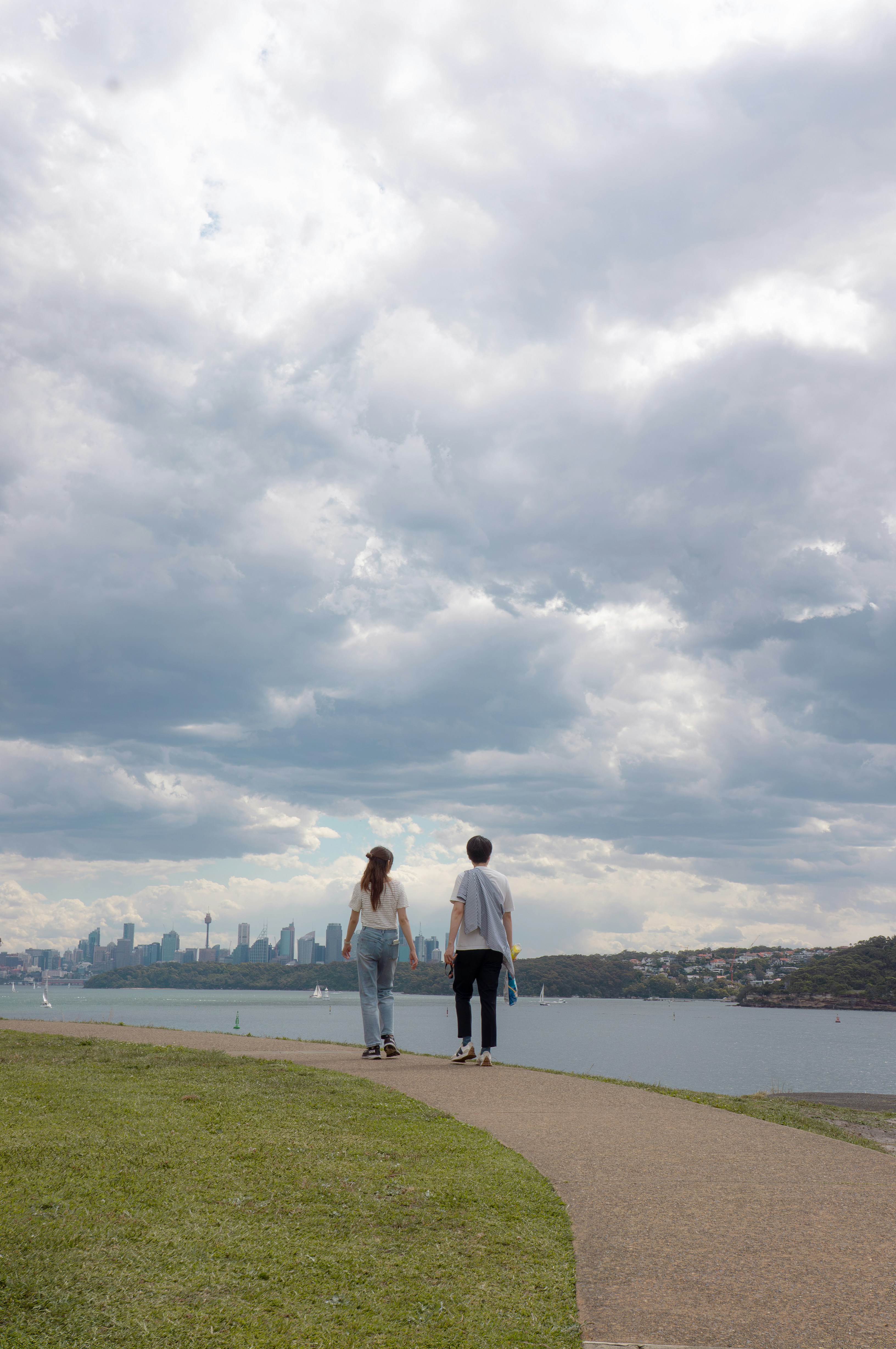 Evening Lake Walk: A Couple on a Cloud-Scattered Riverside Path Toward the City