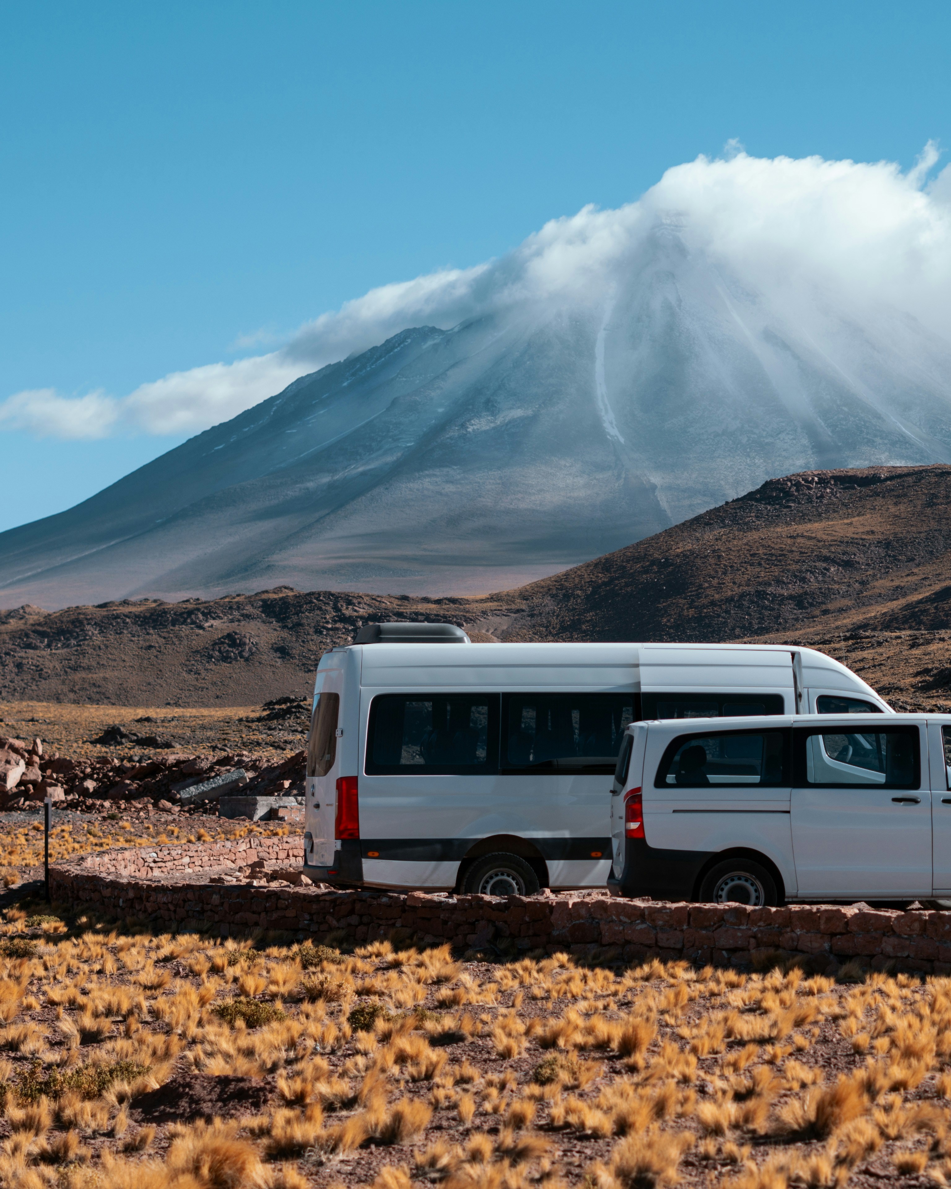 Vanlife at the Foot of a Smoking Summit: White Vans on a Desolate Volcanic Plain