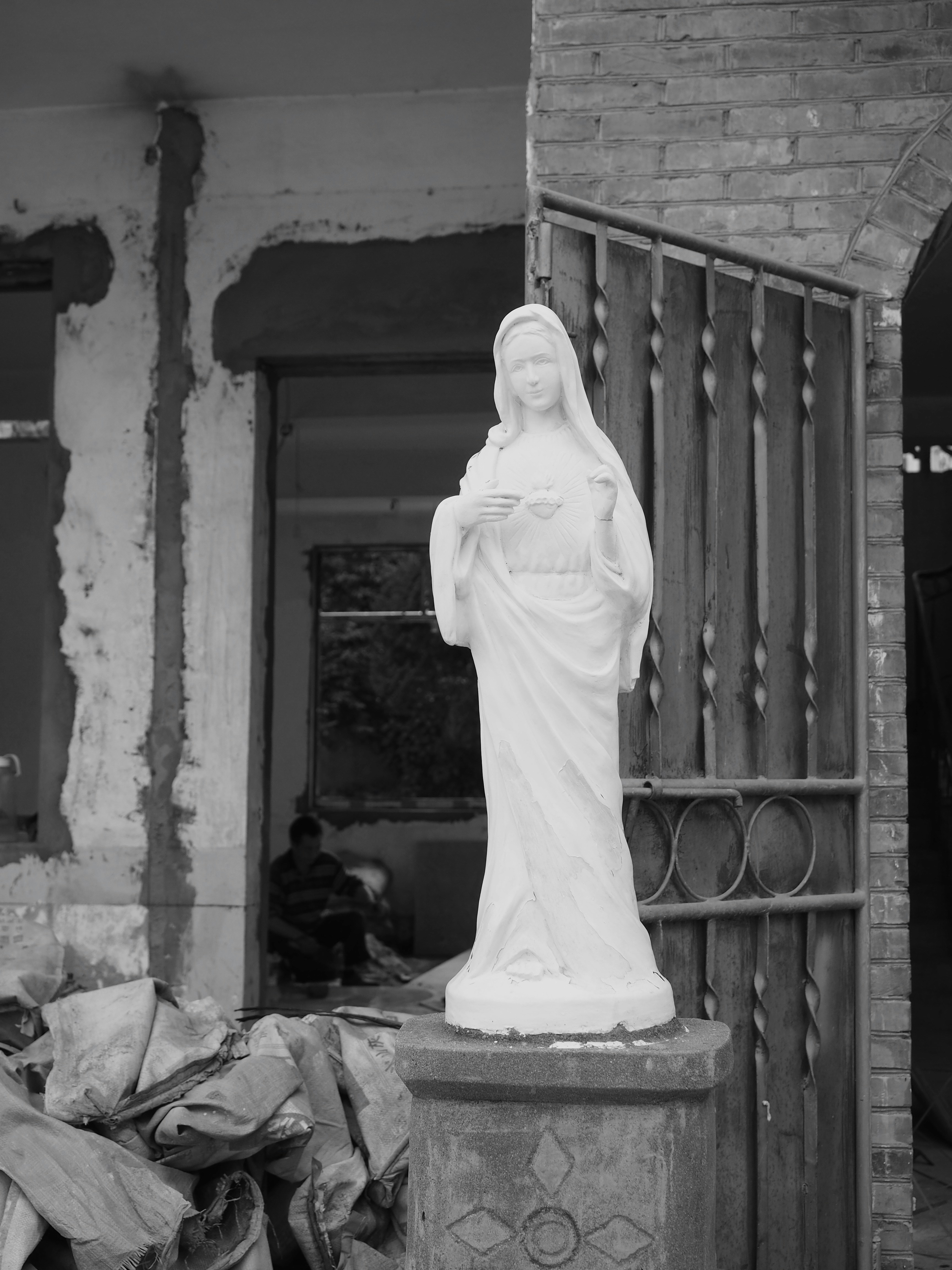 Hope in Concrete: Virgin Mary Standing Guard by a Dilapidated Gate