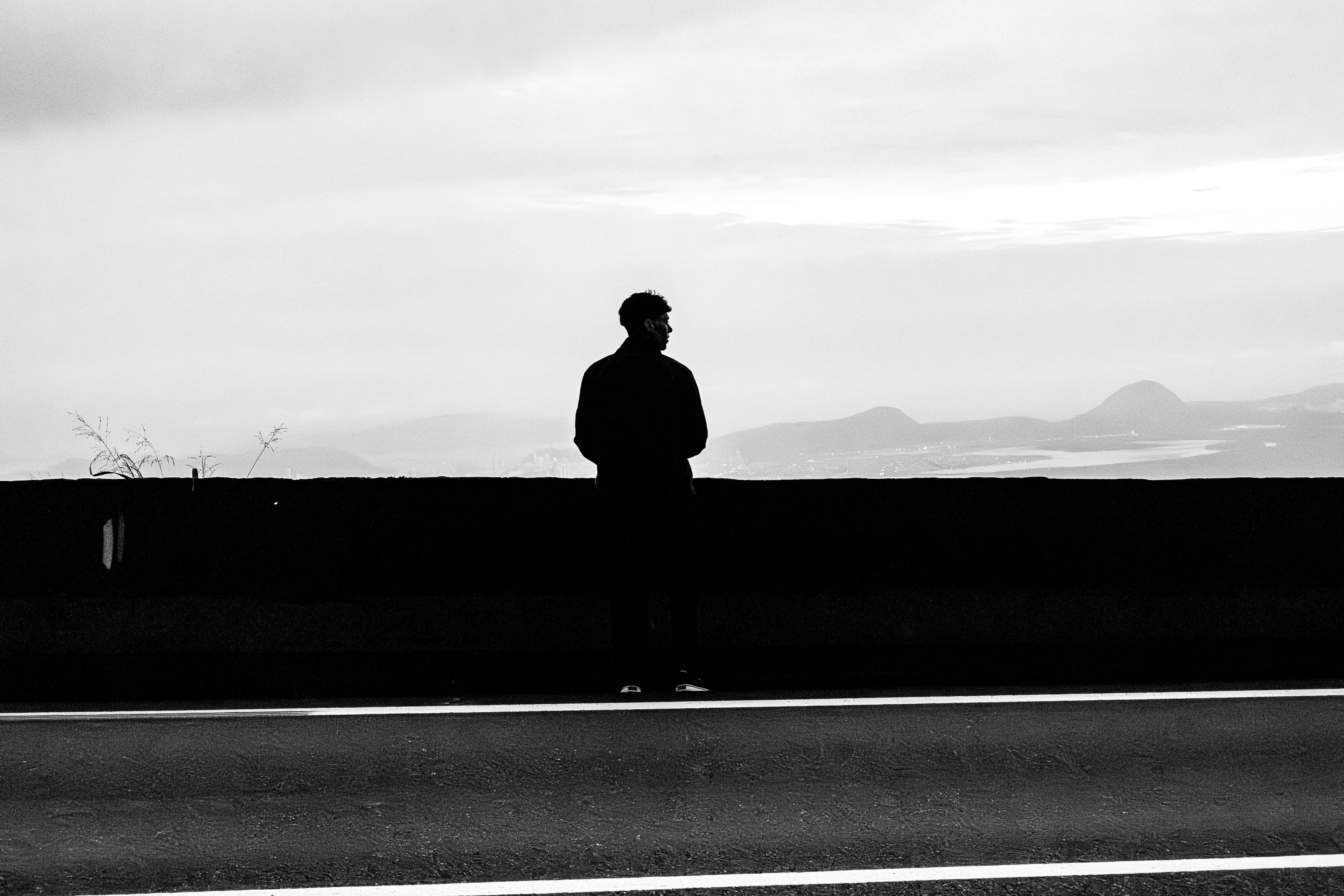 Solitary figure in silhouette, contemplating a hazy, distant, tranquil landscape.