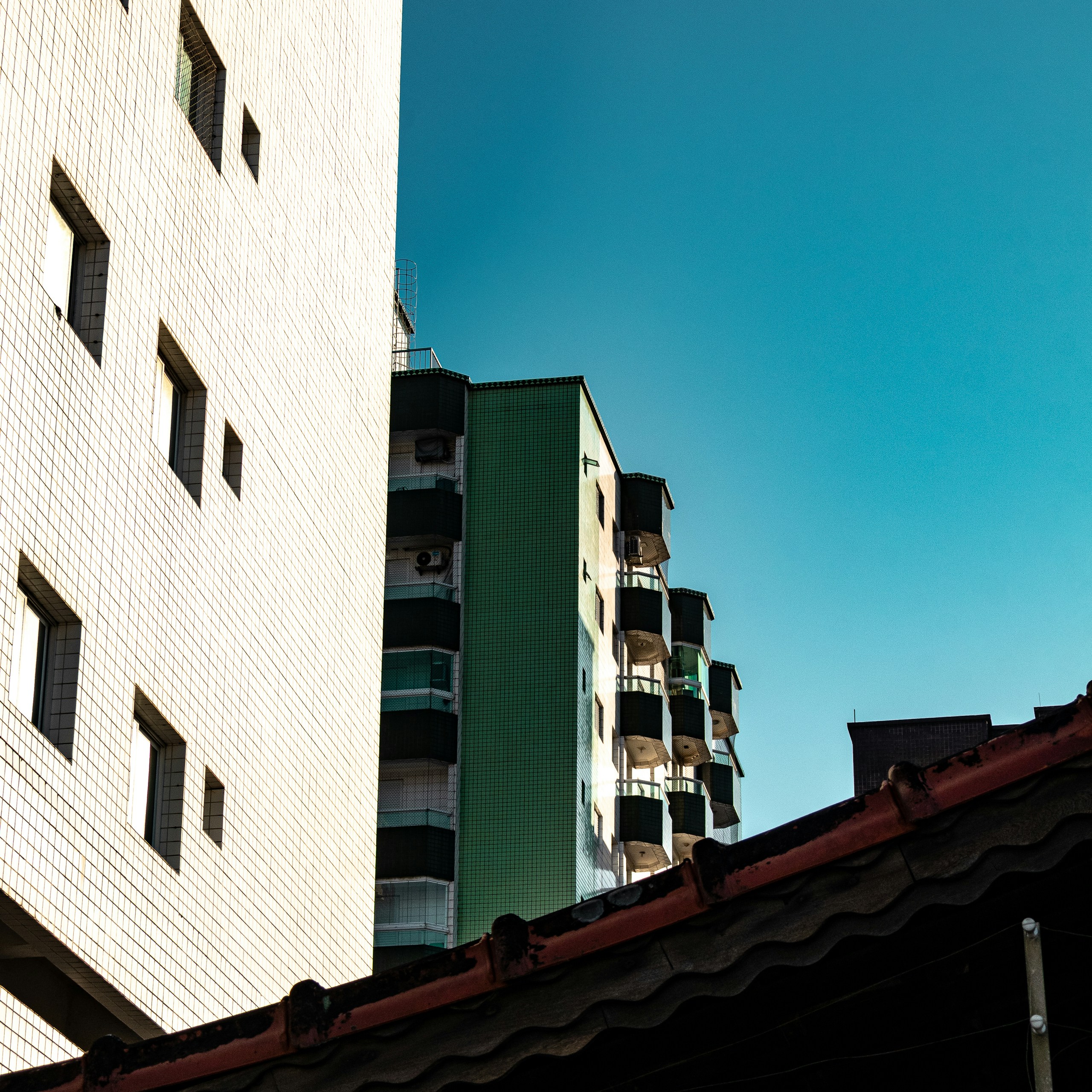 Stark urban forms and vivid blue sky, framed by an aged rooftop.