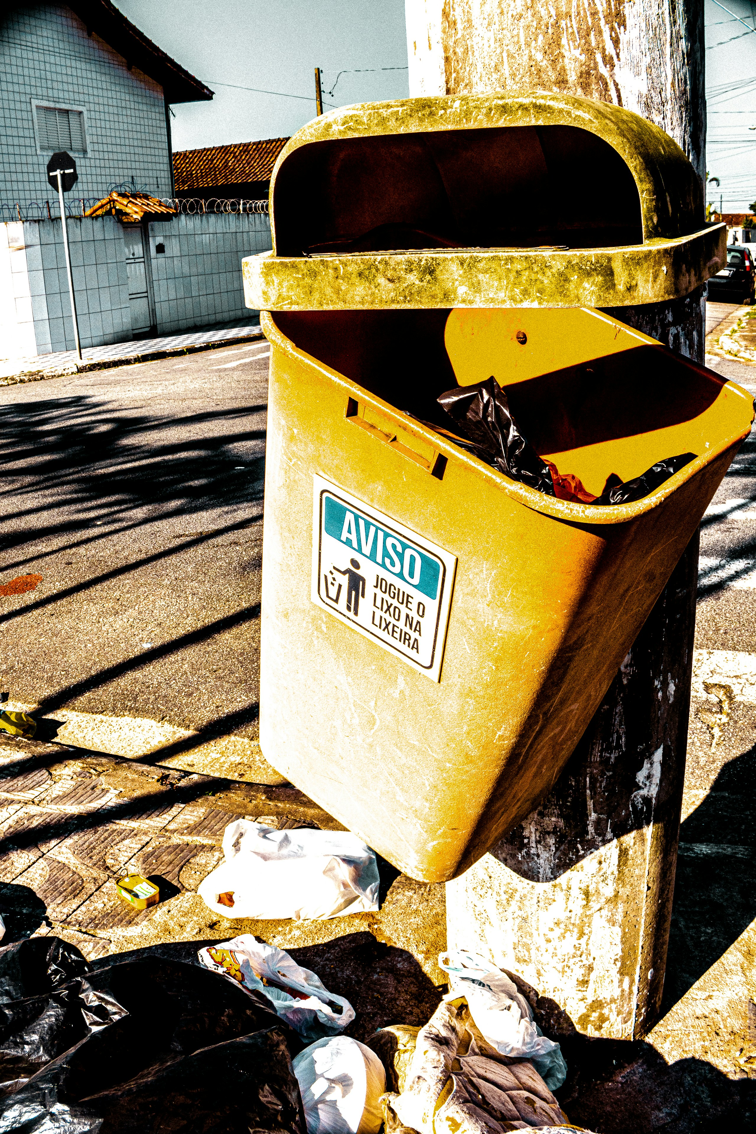Urban neglect: yellow bin overflowing with refuse, stark visual contrast.