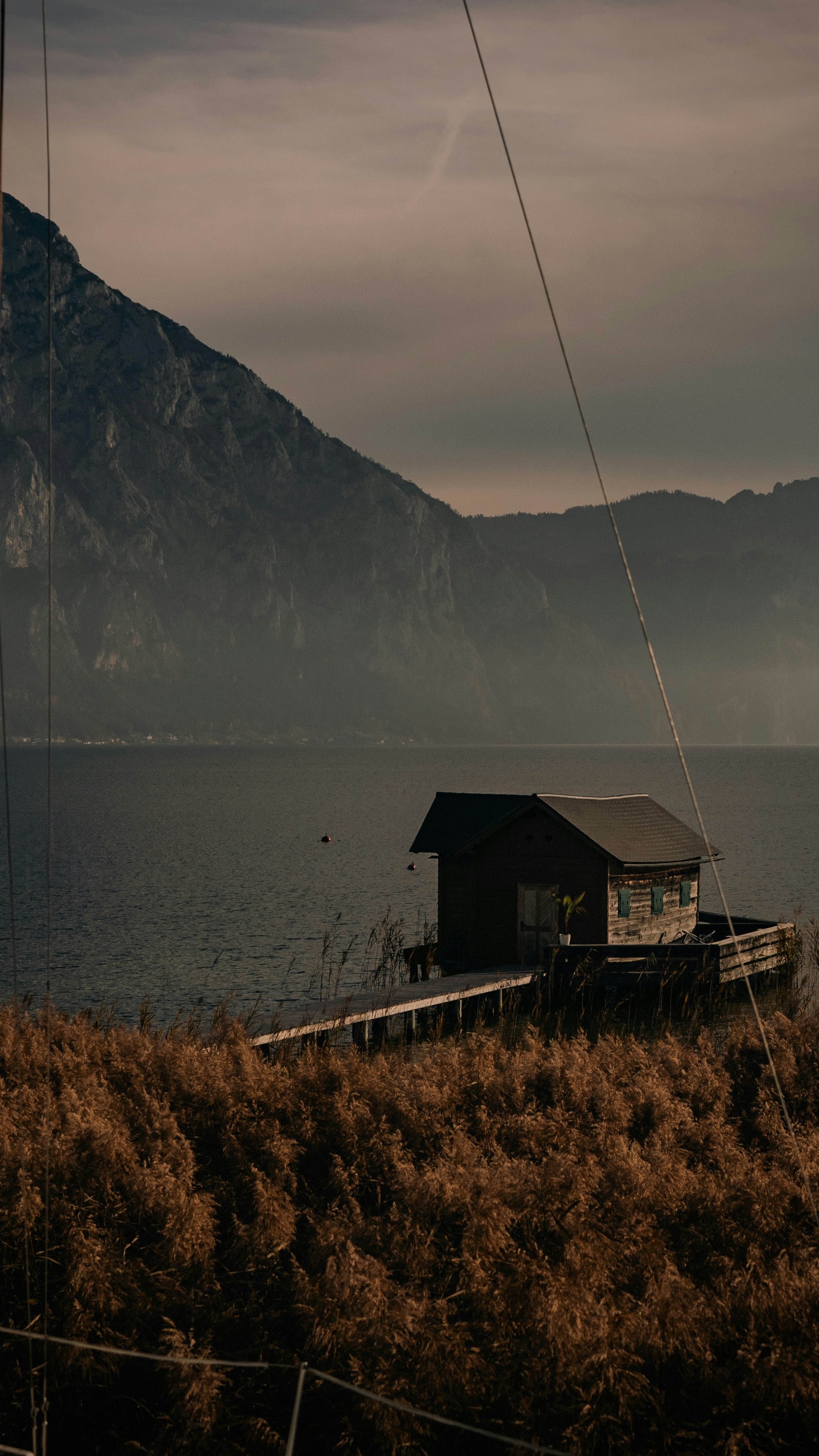 Weathered Dockside Hut Beneath a Veiled Mountain Lake at Dusk