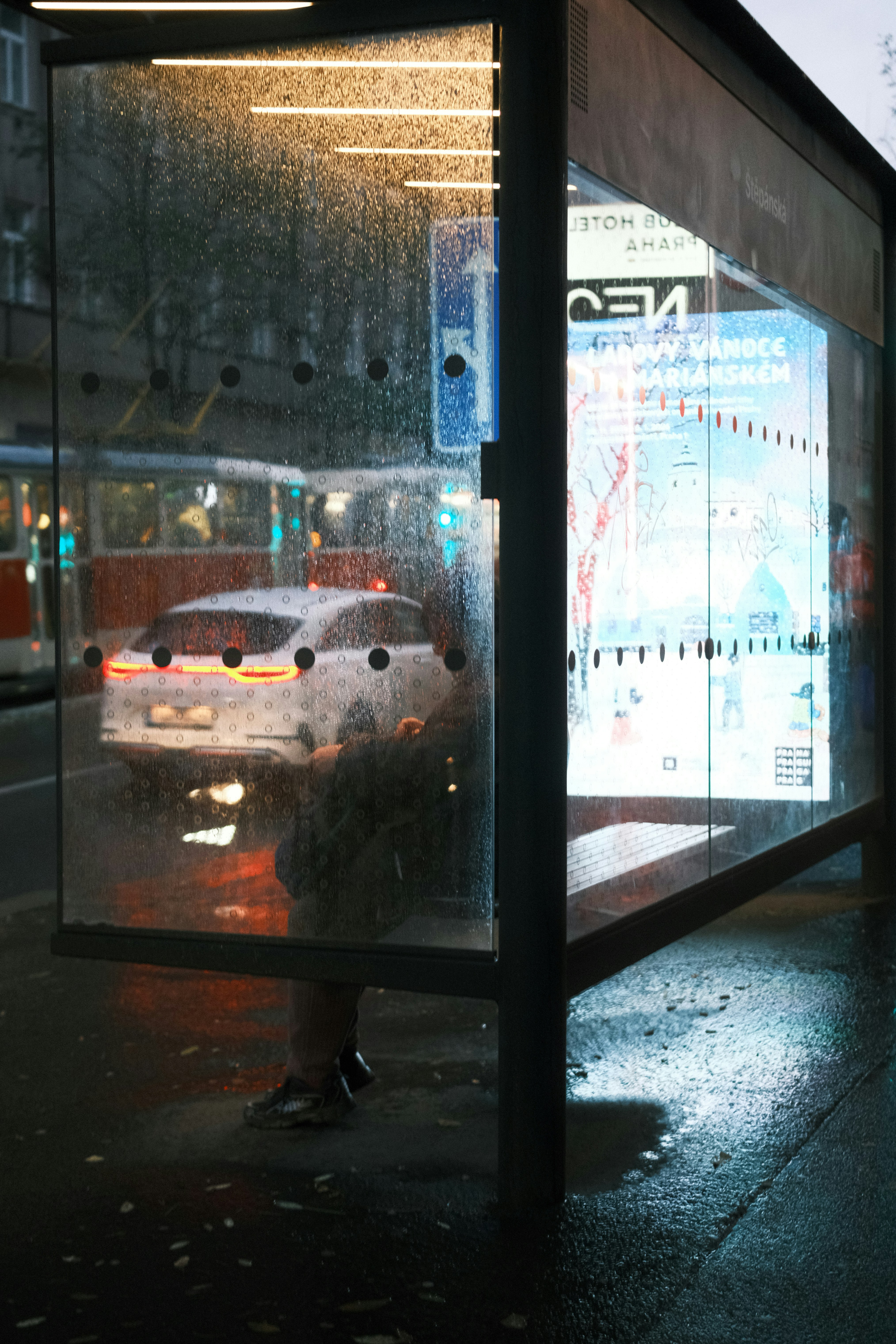 Bus stop shelter during rain at night with illuminated advertisement