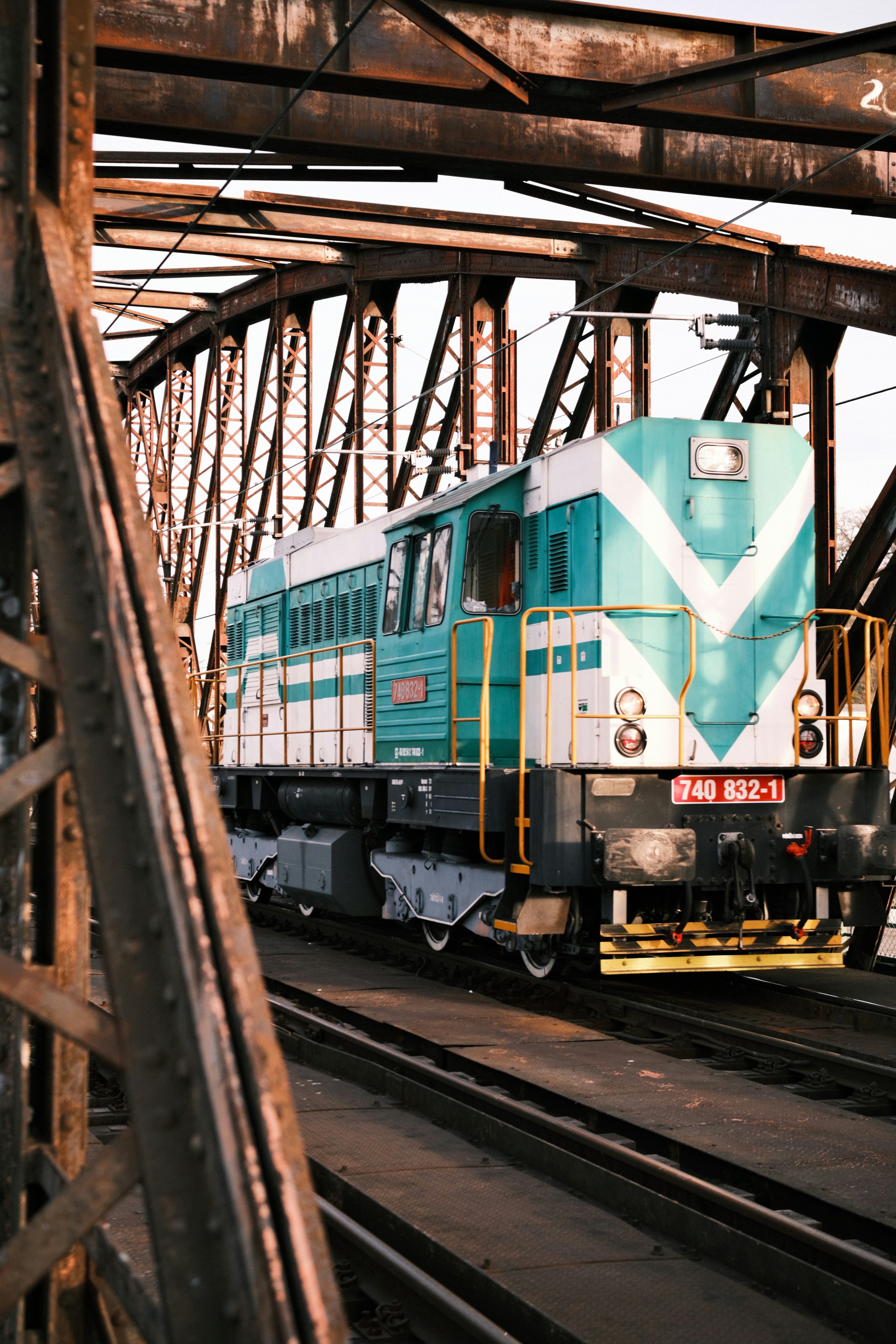 Teal diesel on a rusted iron bridge: locomotive framed by lattice and light