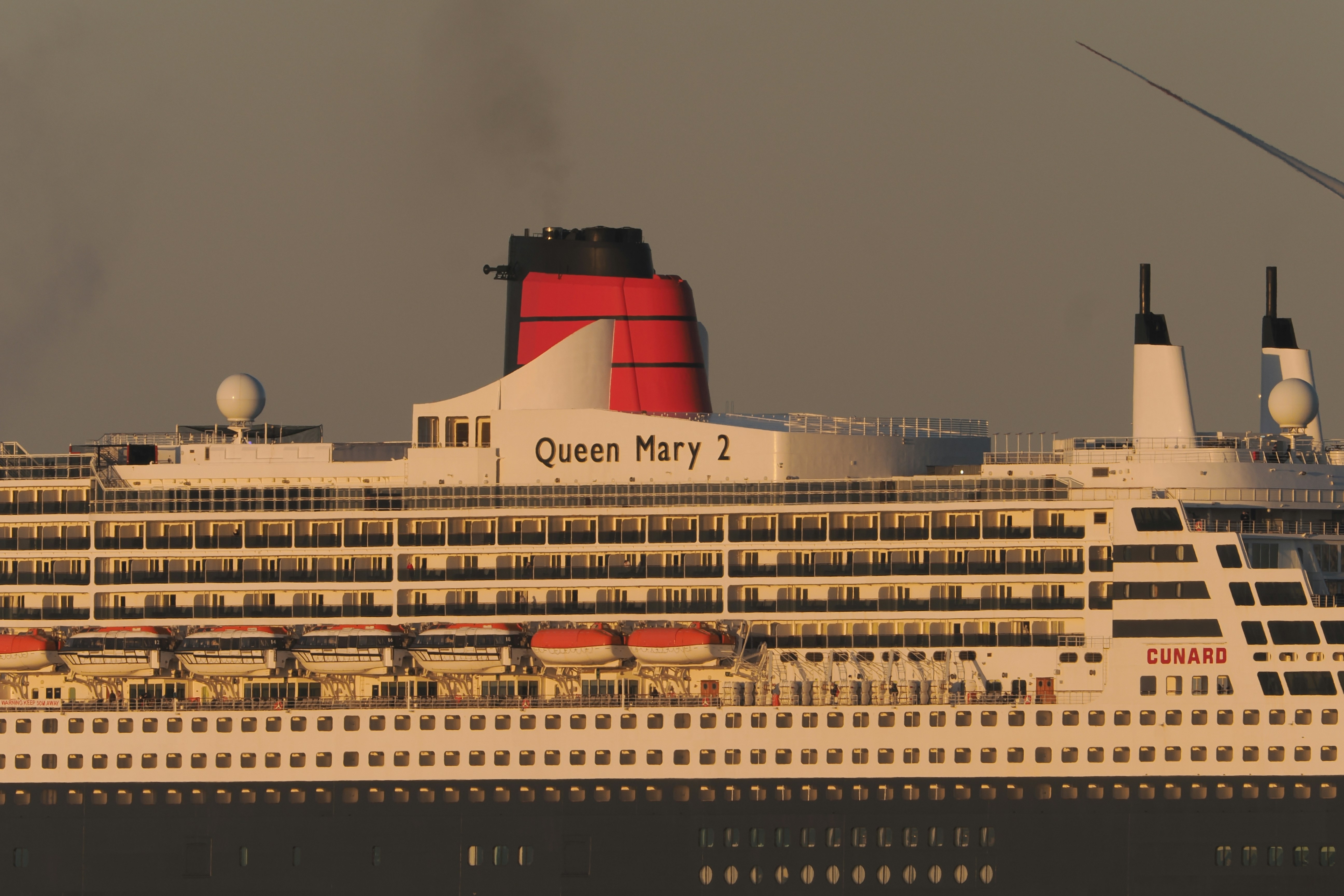 Queen Mary 2 under amber harbor light: the crimson funnel among stacked decks