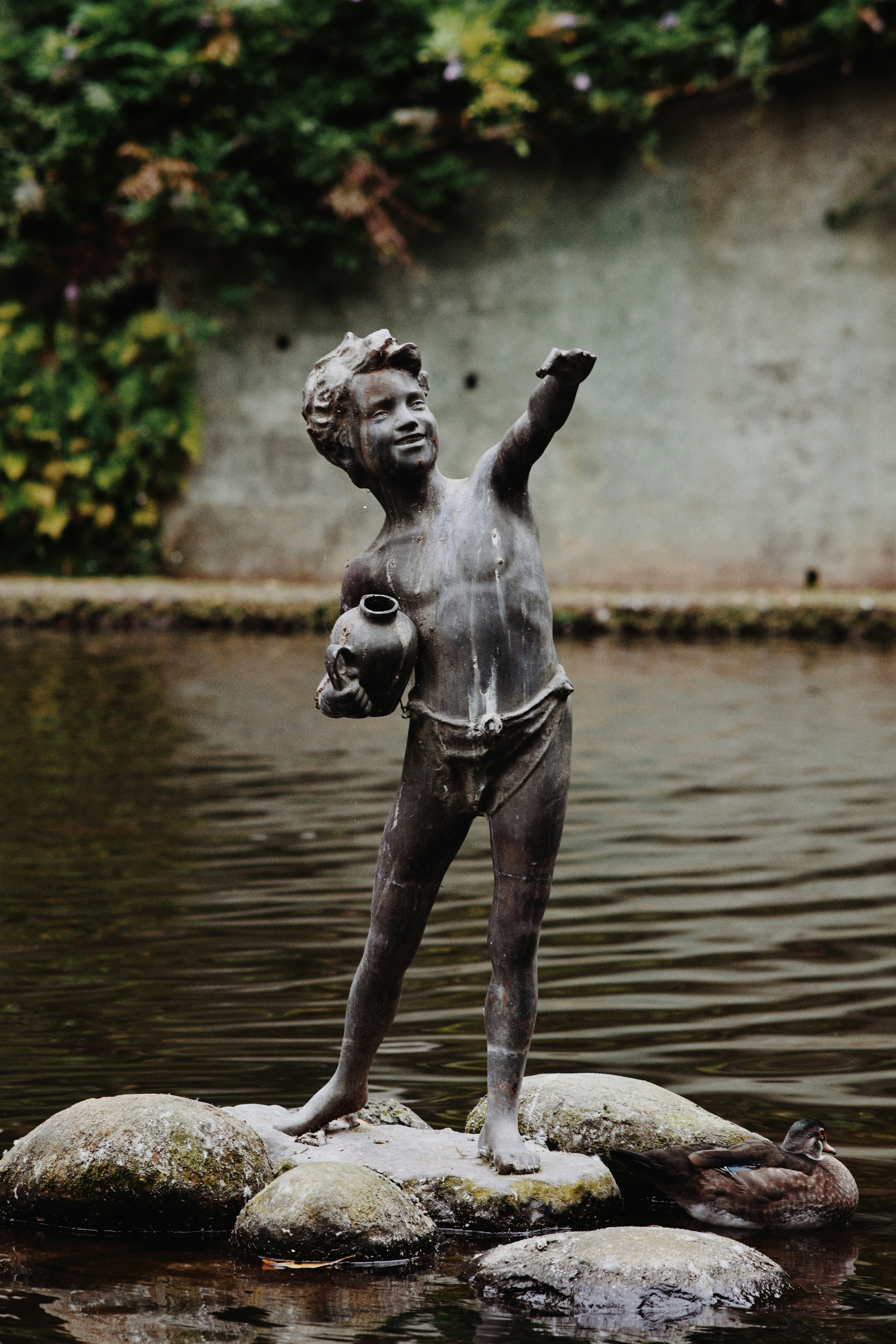 Bronze Child on Pebble Island Reaches Across a Quiet Pond