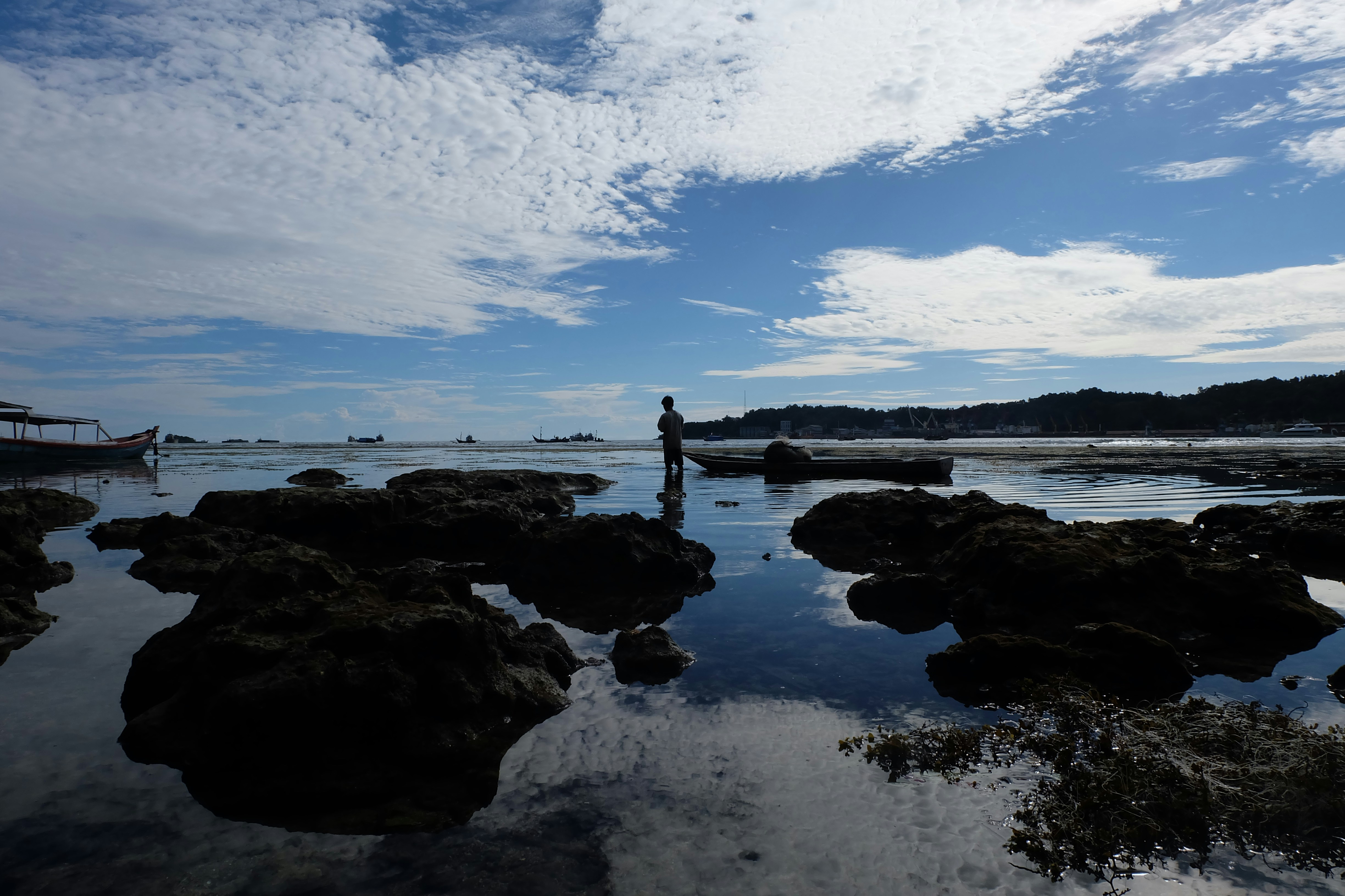 Lone Figure on a Tidal Rock Ridge Beneath a Sky of Moving Clouds