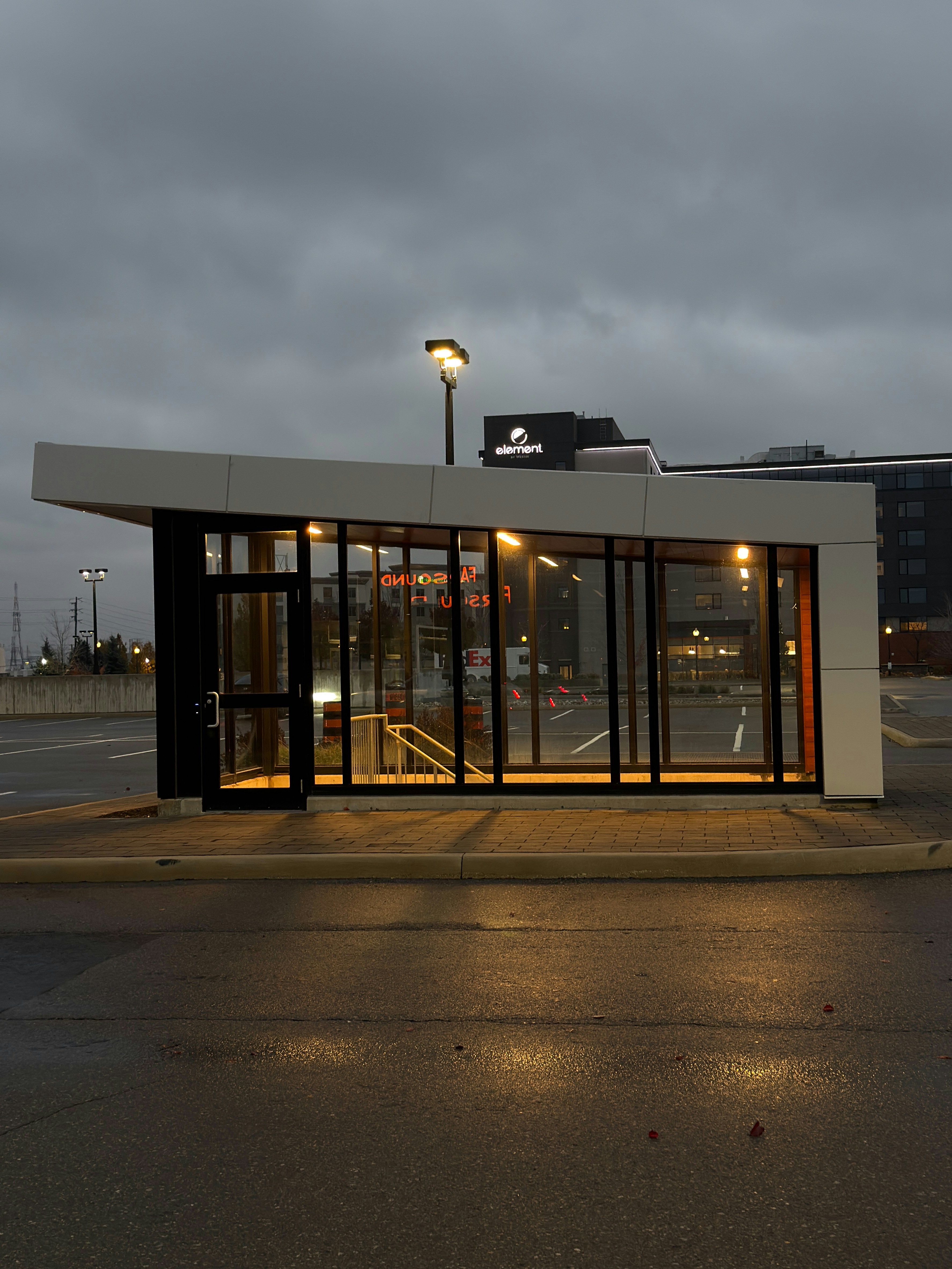 Glass Capsule at Dusk: A Modern Kiosk in a Quiet Parking Lot