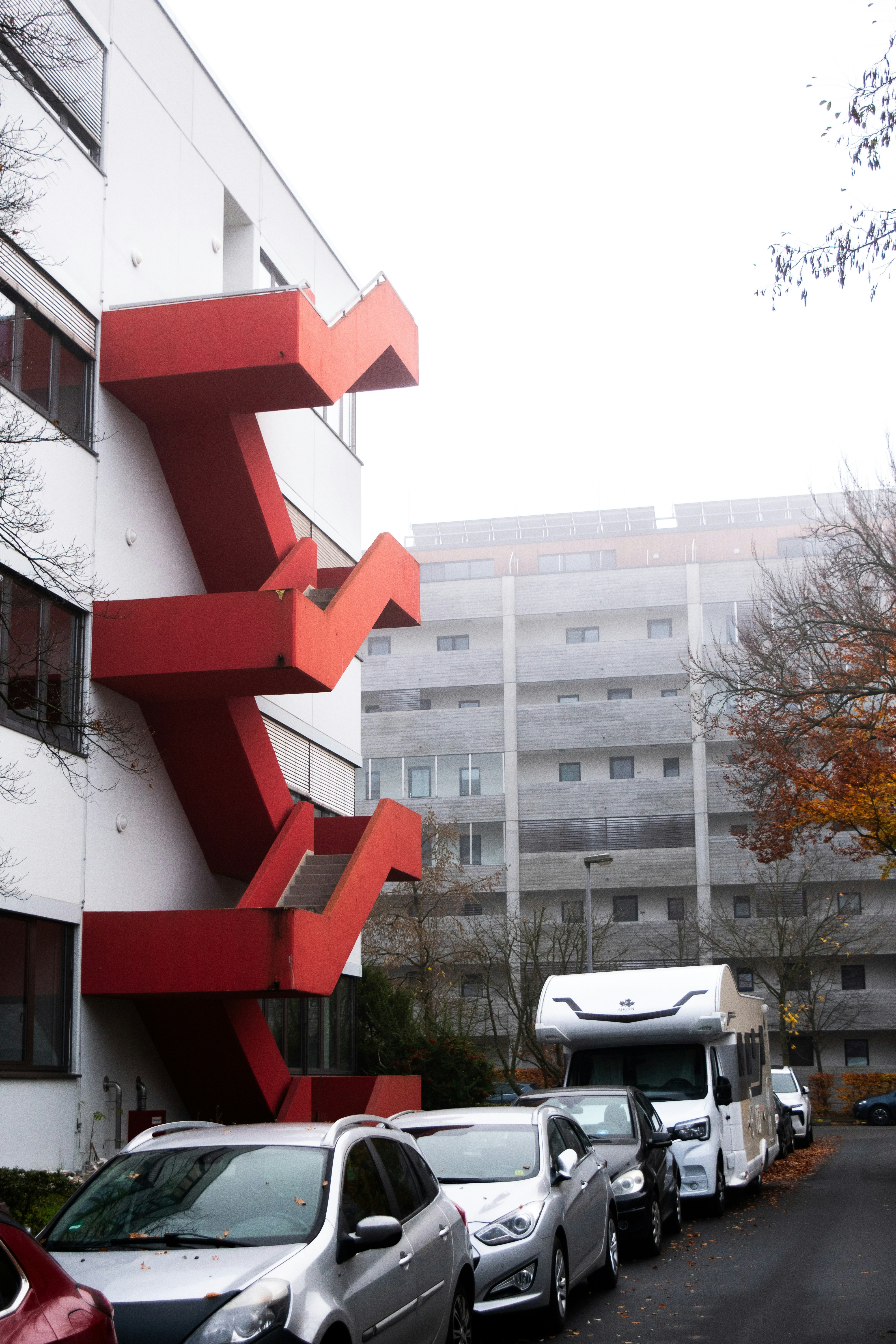 Crimson Zigzag Staircase Framing a White Building’s Geometry