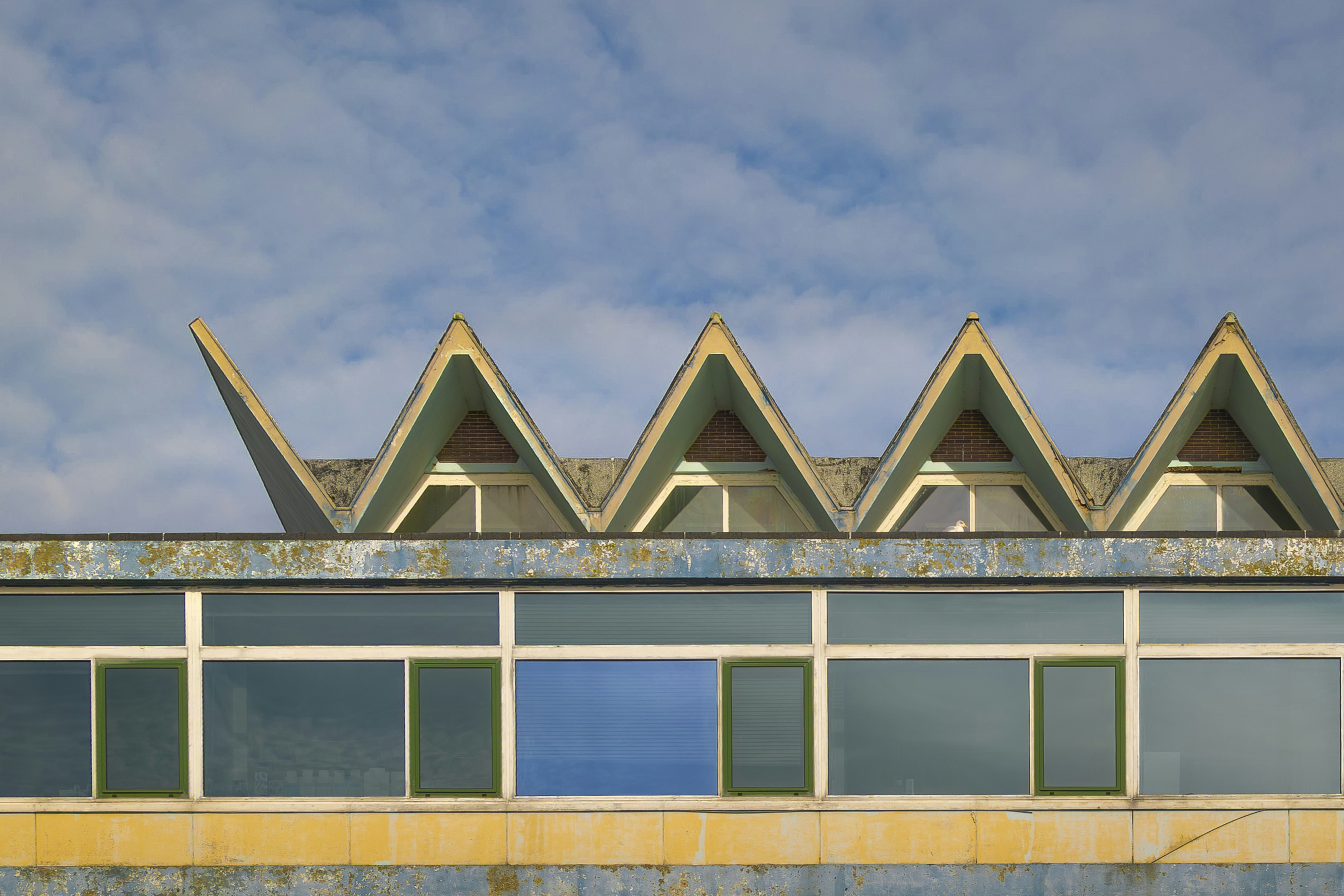 A geometric detail of the fish auction building in Scheveningen, featuring repeating triangular roof structures and weathered blue façades. Captured in soft daylight, highlighting texture, rhythm, and coastal atmosphere.