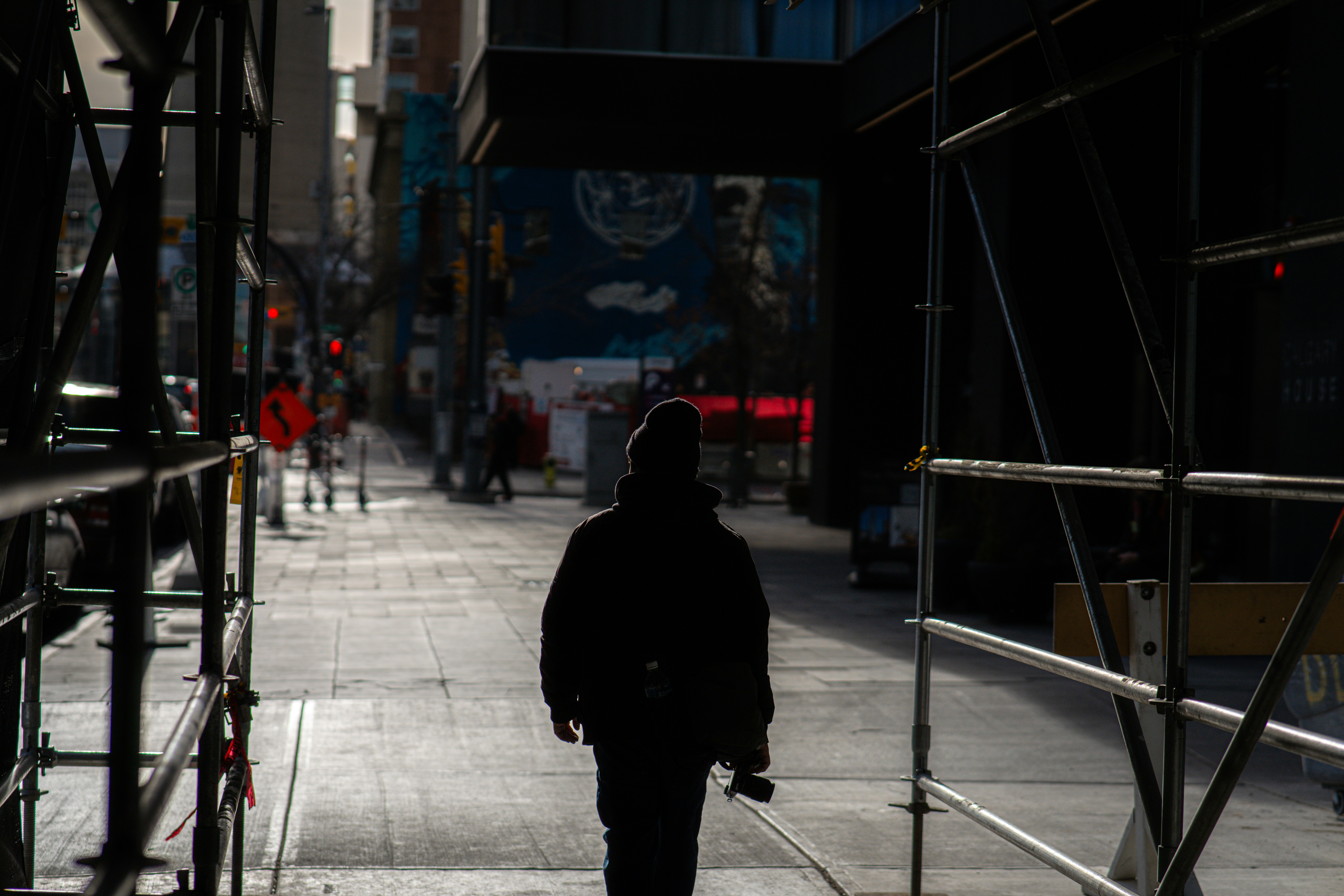 Between Shadows and Light: A Lone Walker in a Scaffolded City Corridor