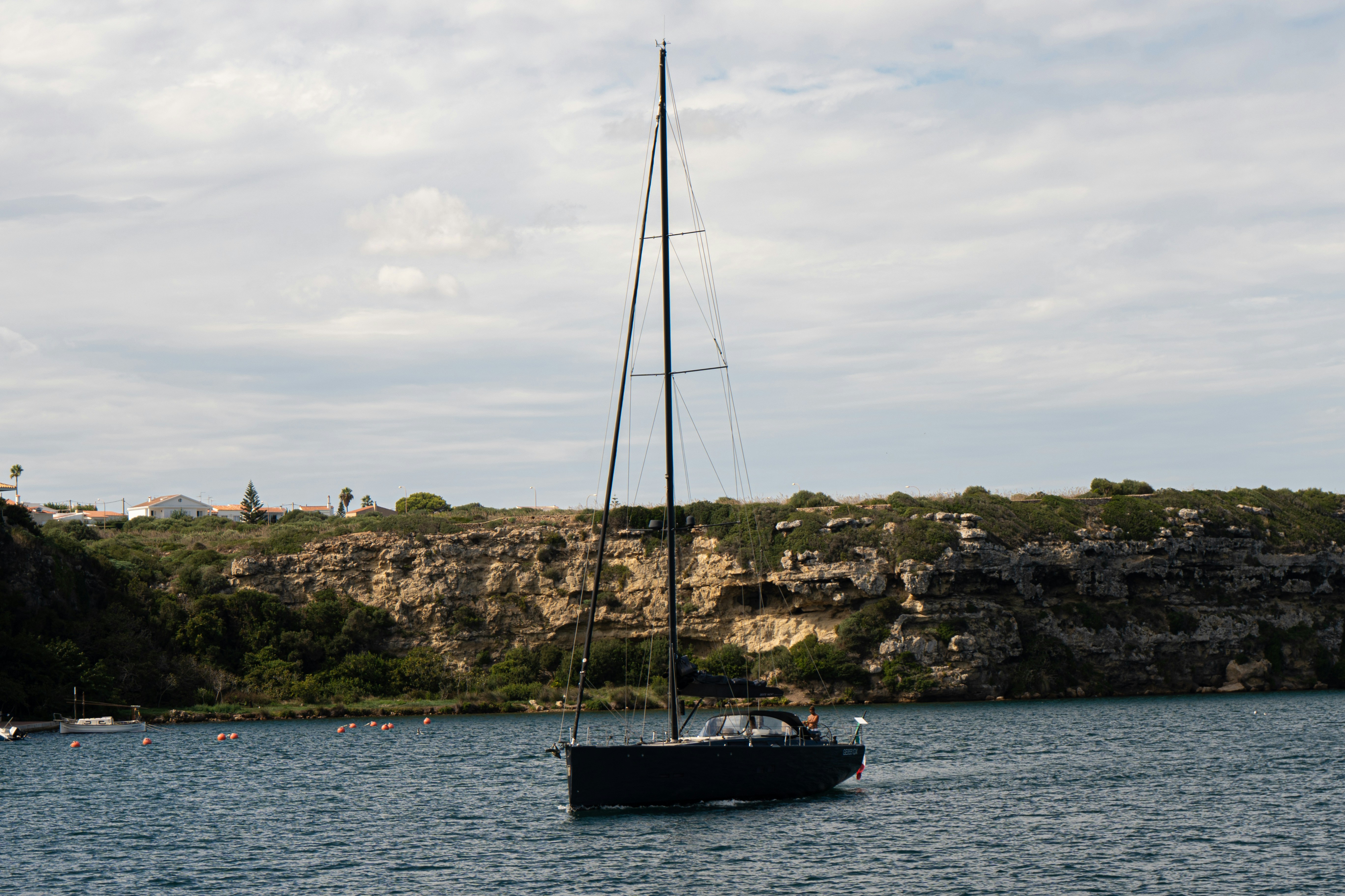 Harbor Solitude: A Sailboat Poised Before Cliffside Calm