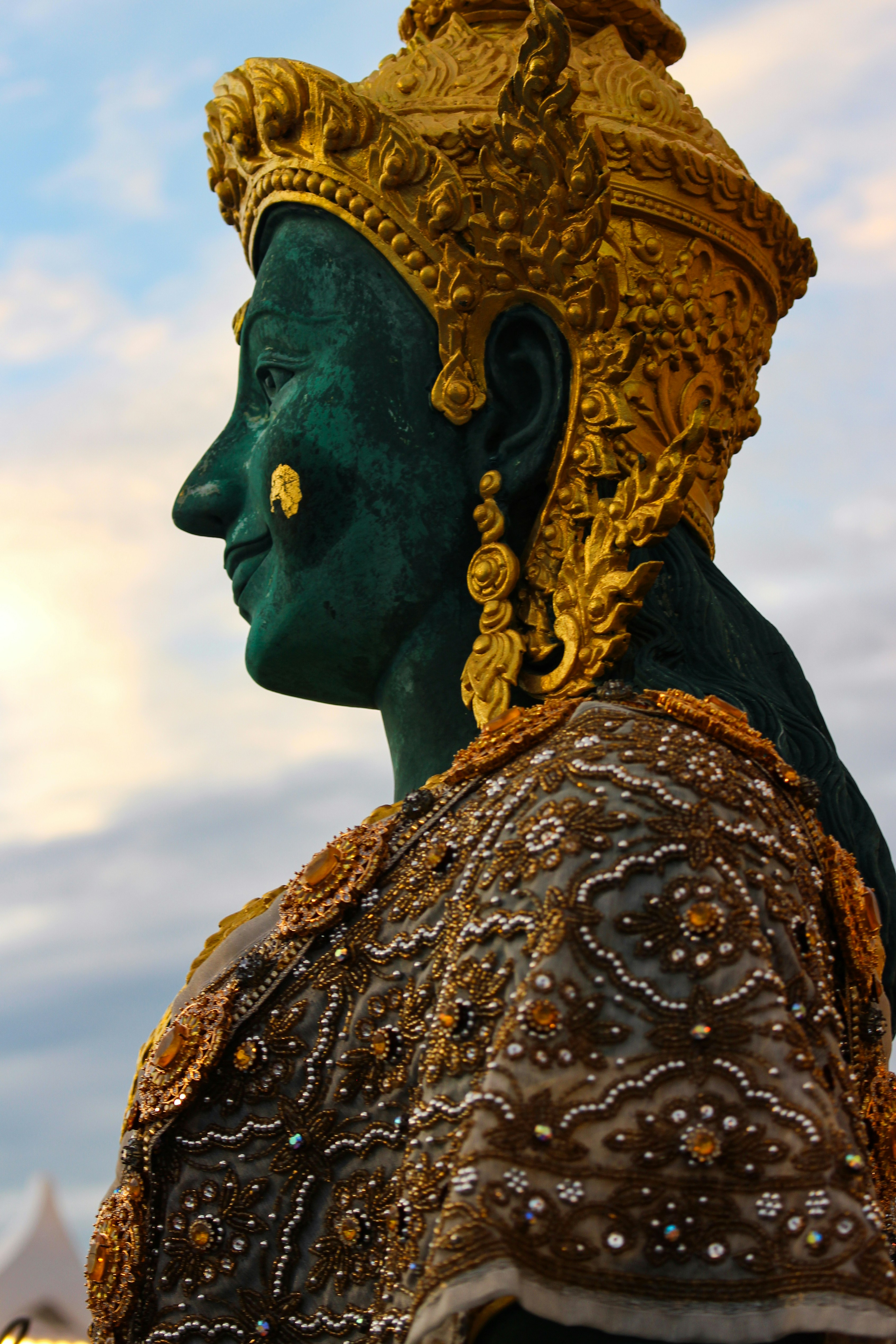 Verdant Deity in Golden Regalia Against a Cloudy Sky