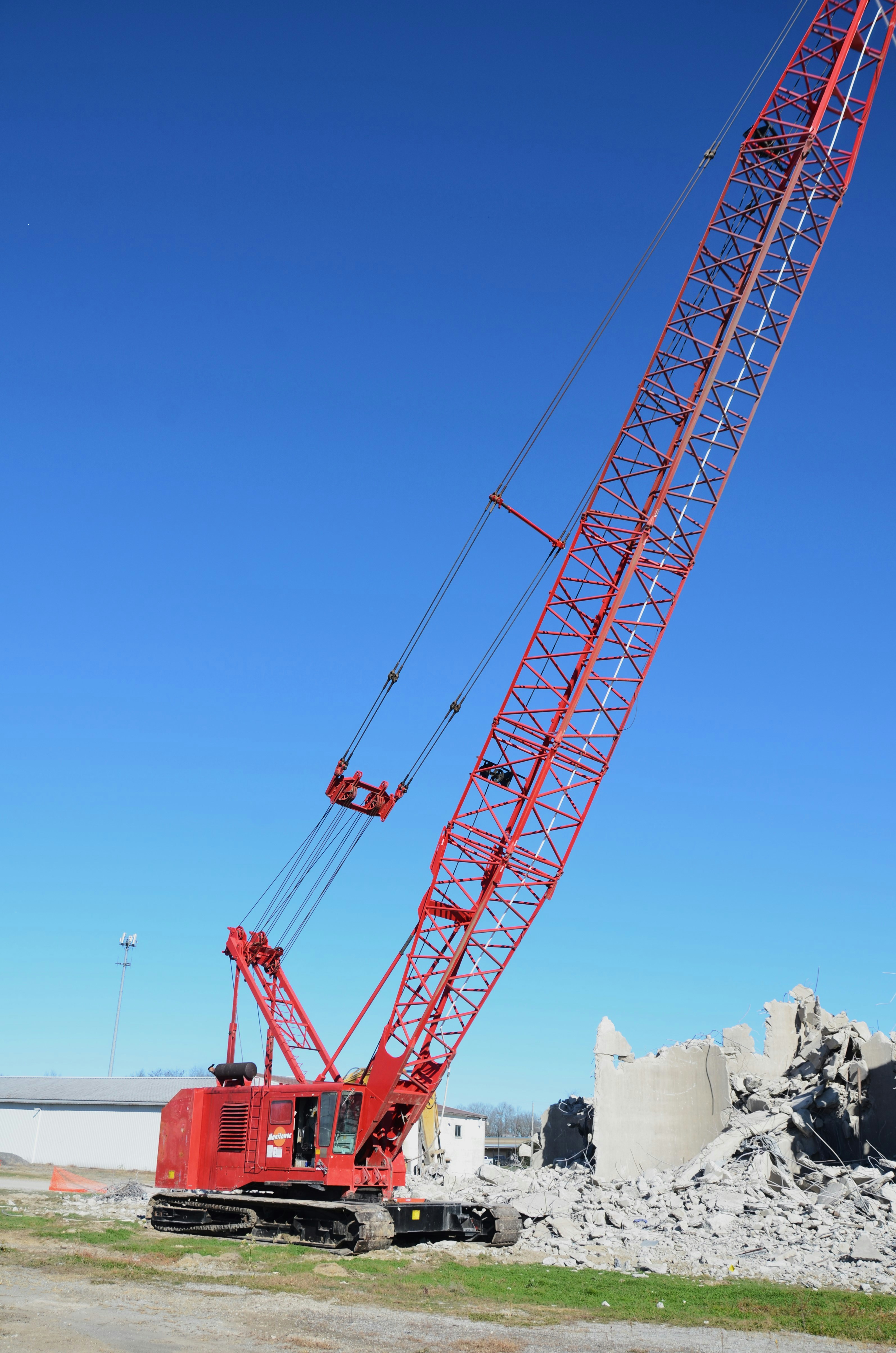 Crimson Lattice Crane Rising Over Rubble Beneath a Clear Blue Sky