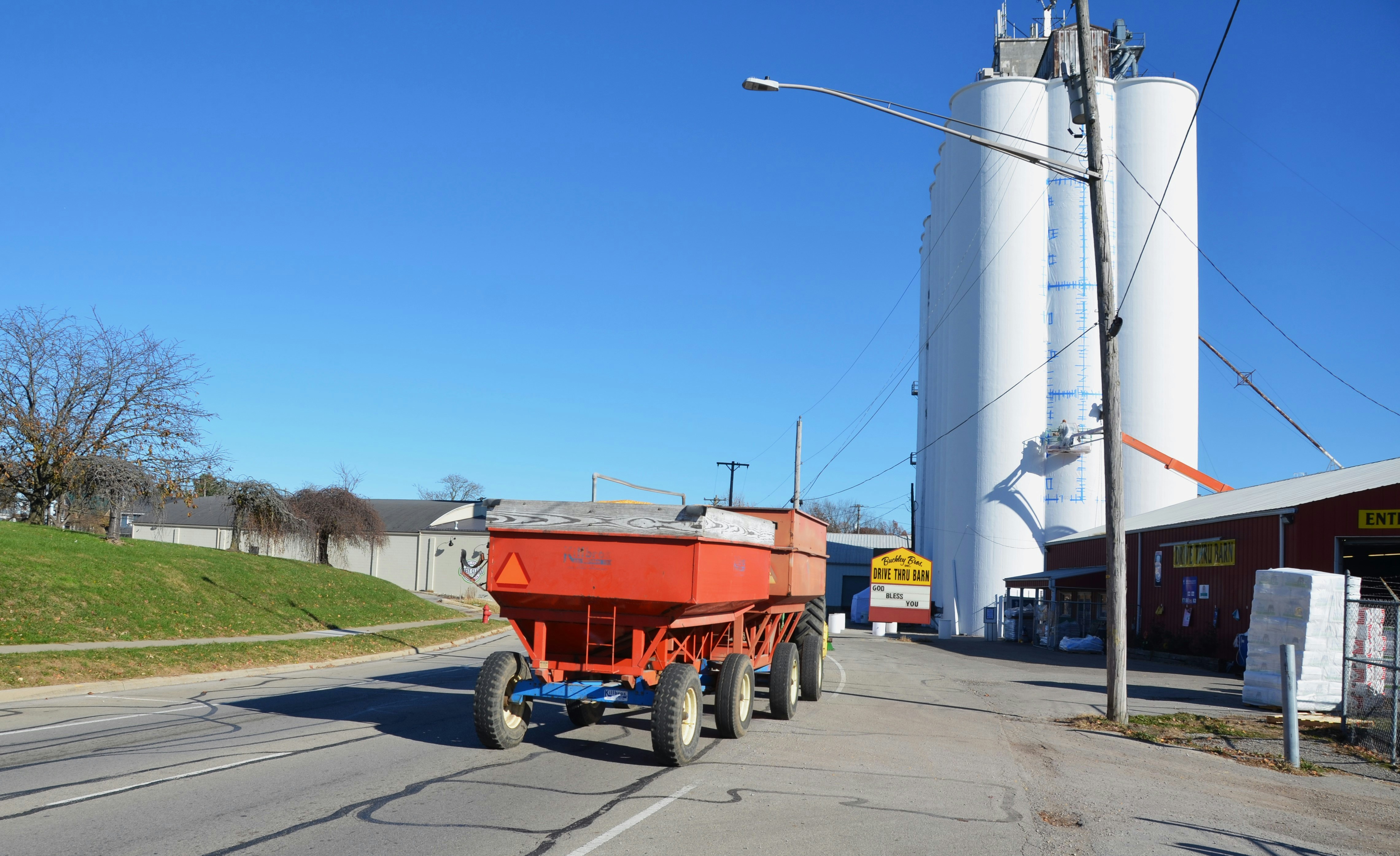 Crimson Grain Trailer Rounds the Silos Under a Clear Midday Sky